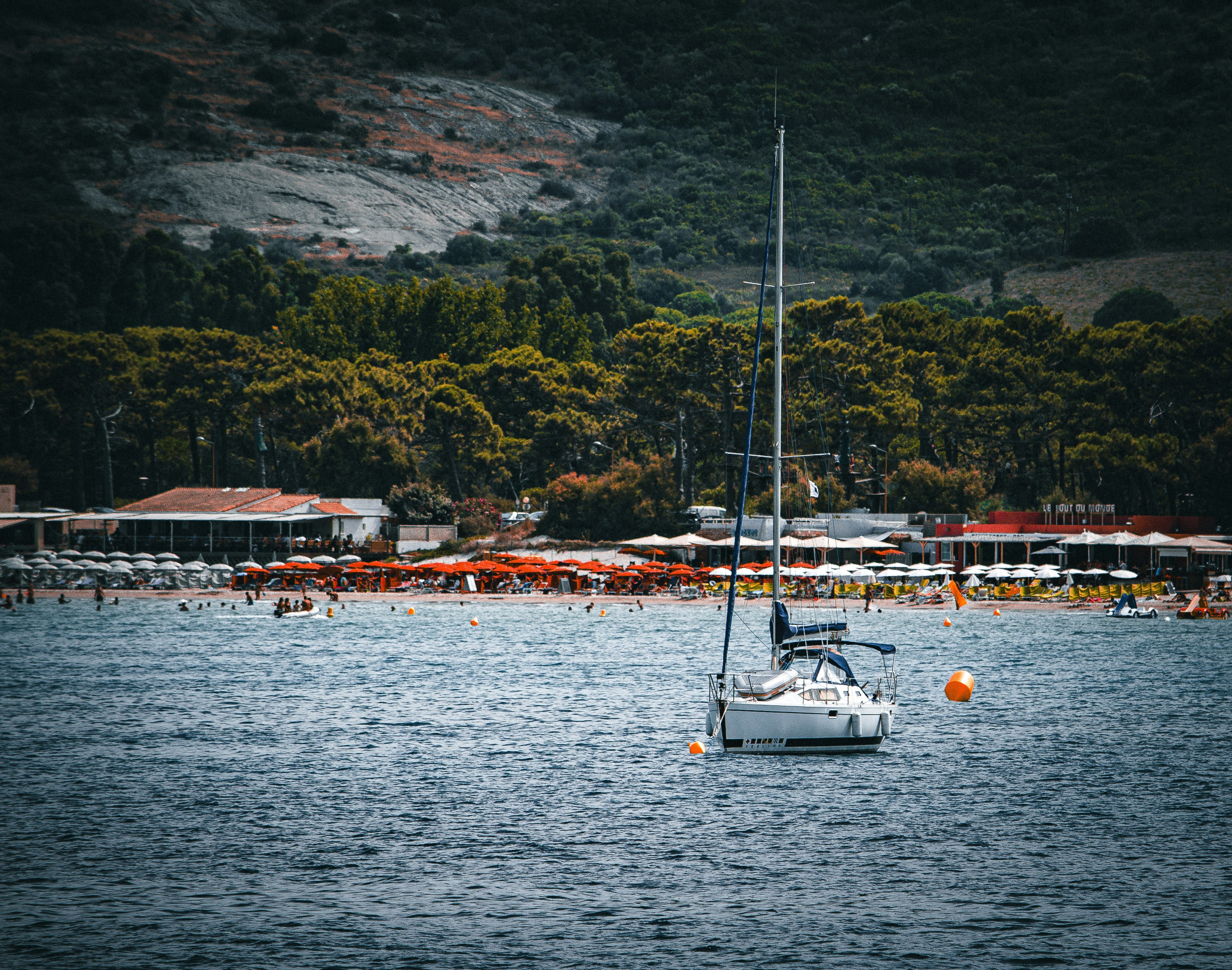 Sailboat Anchored Along a Busy Beachfront Under a Quiet Sky