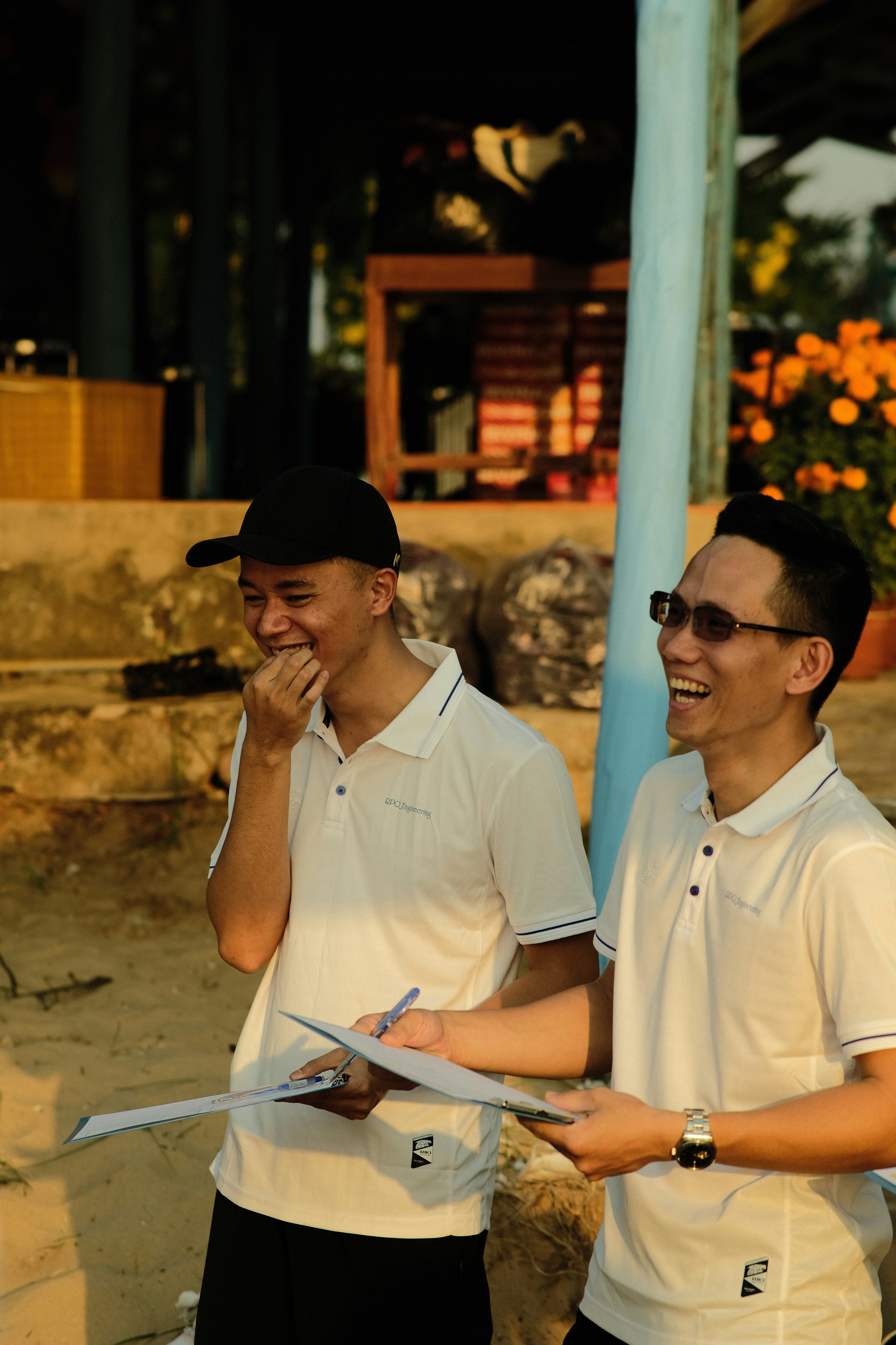 Seaside Briefing: Two Friends Laugh as Papers Pass Under Golden Hour Light