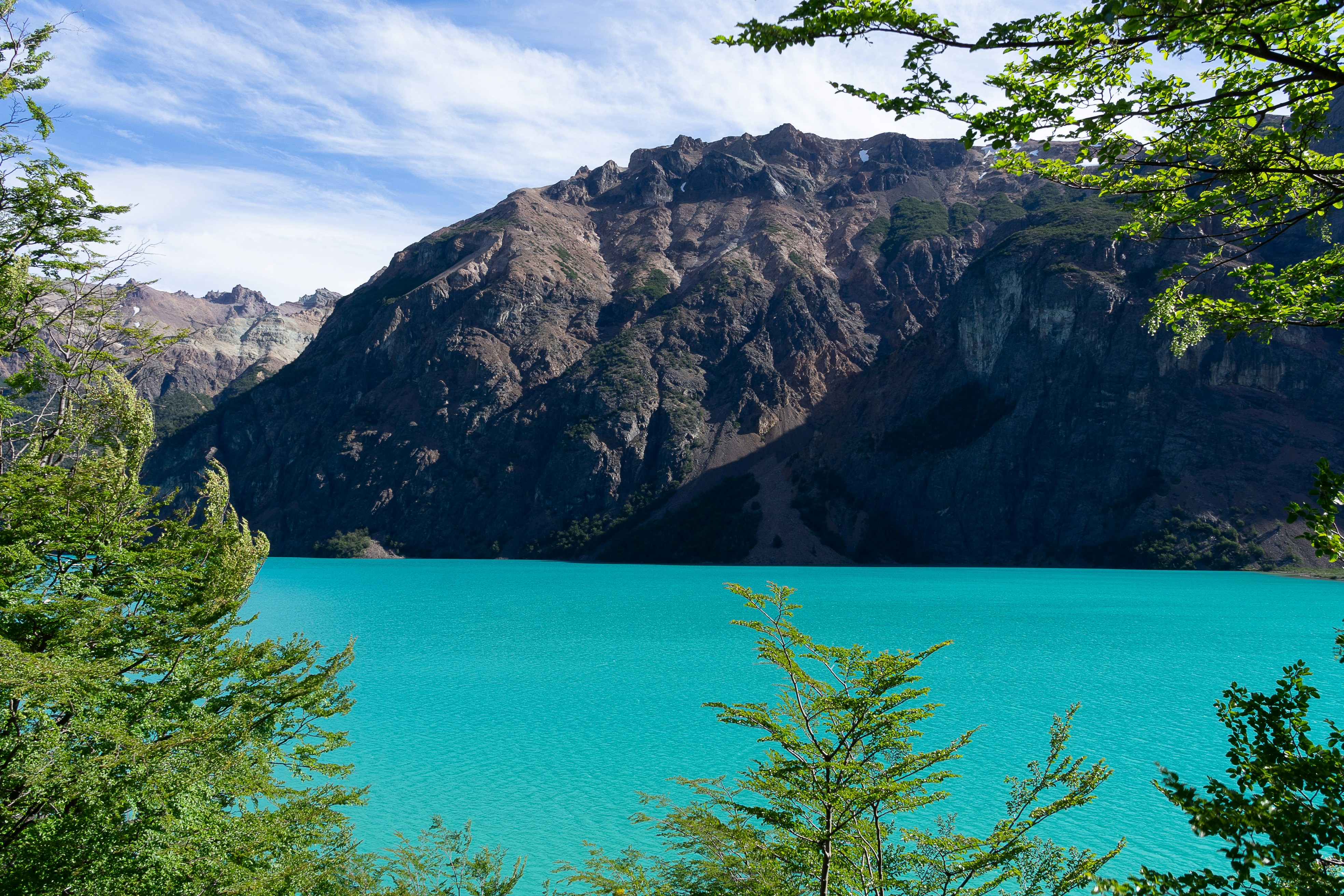 Turquoise lake framed by towering mountains and lush greenery under a bright sky.