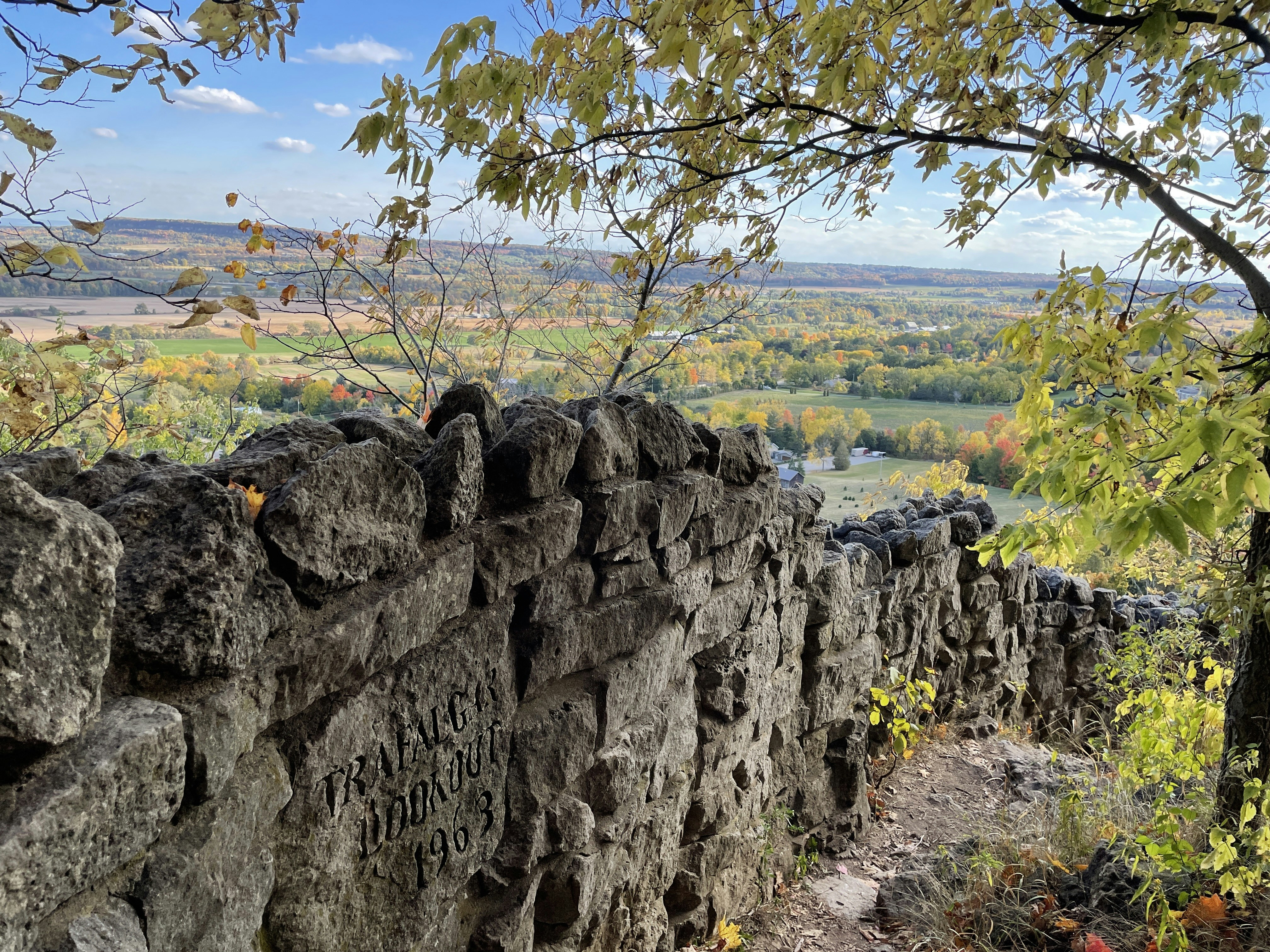 Stone wall overlooking a vibrant autumn landscape under a clear blue sky.