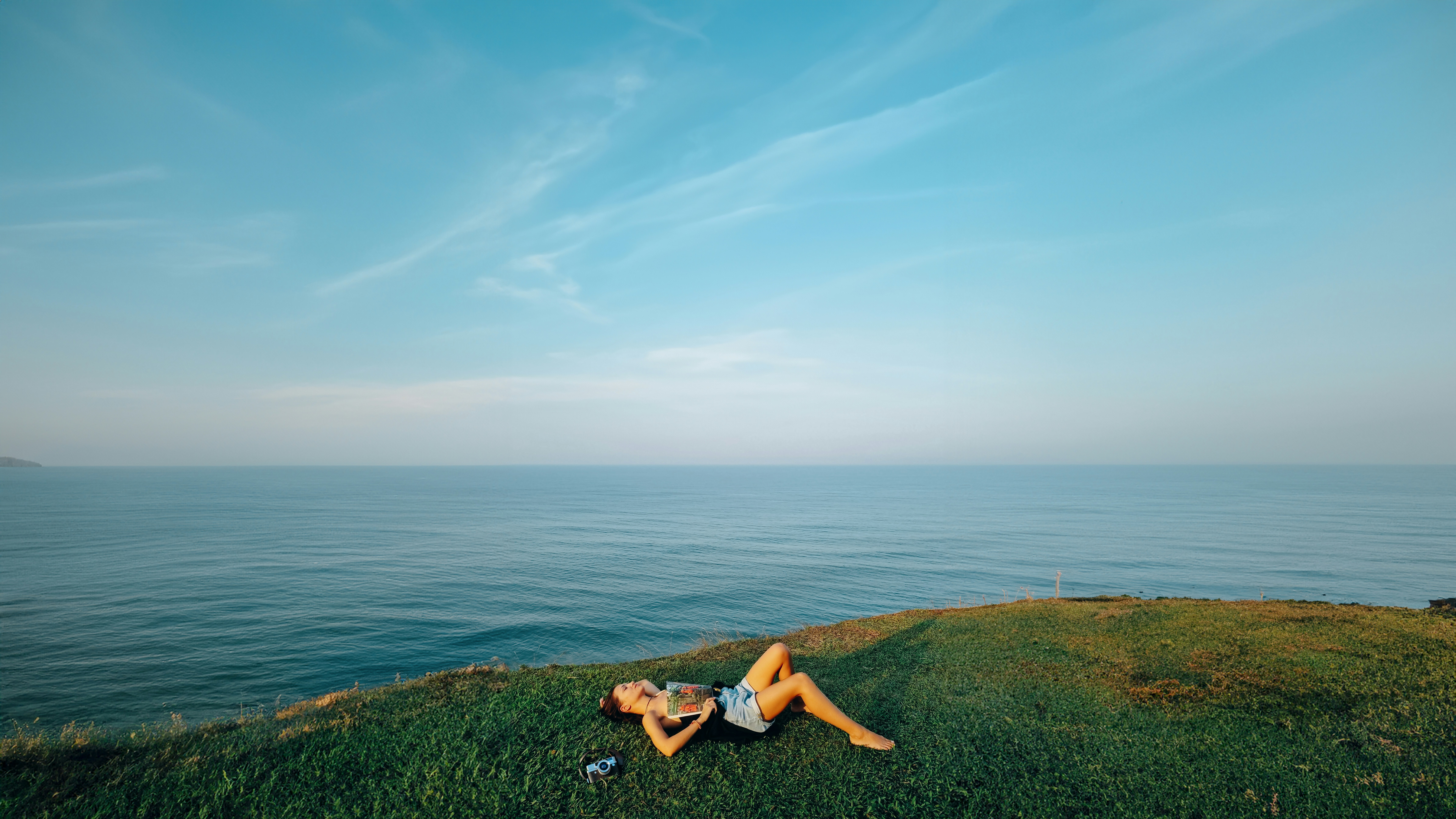 A woman laying on top of a lush green hillside next to the ocean photo ...