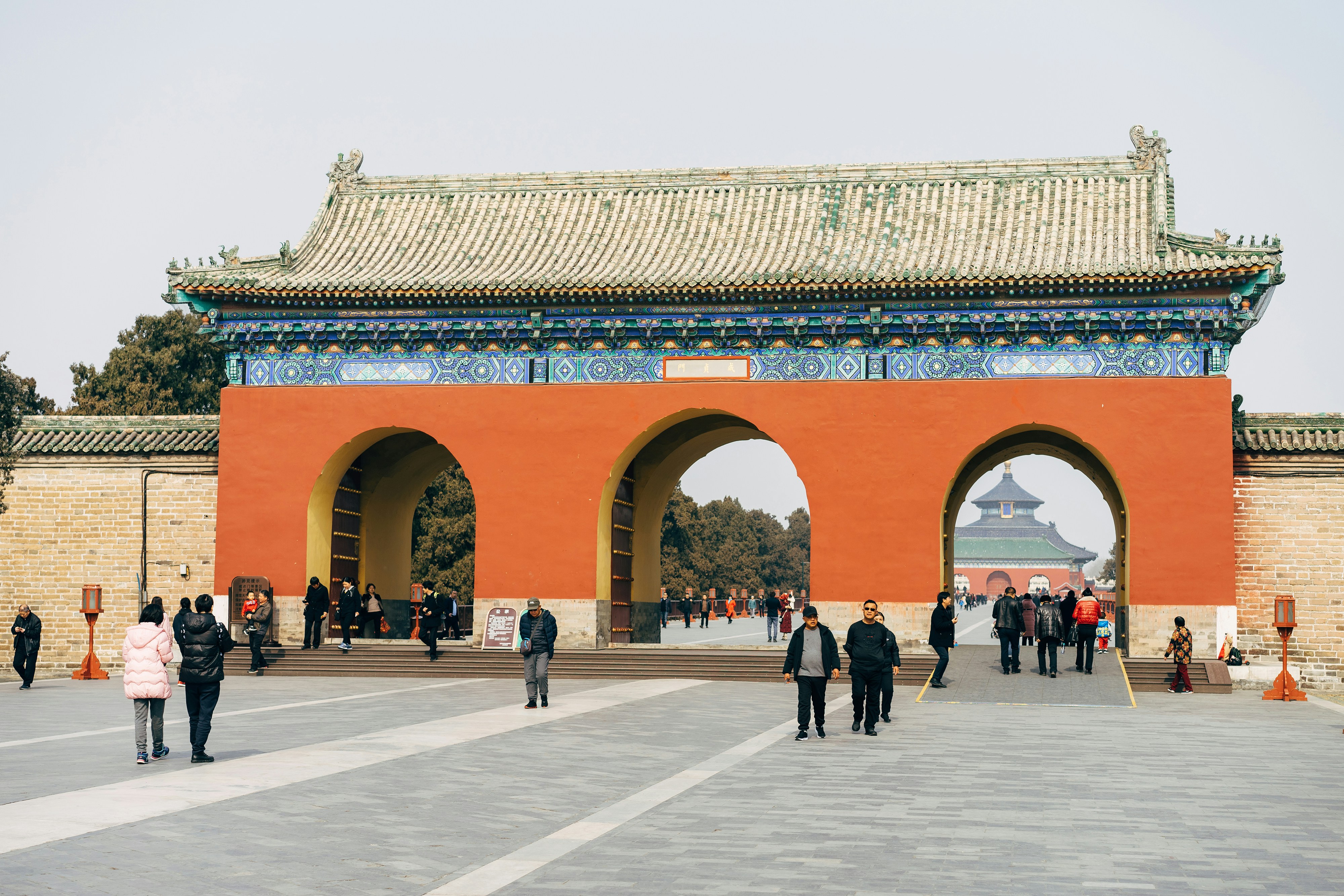 Historic arched gateway with ornate detailing framed by a distant temple under a clear sky.