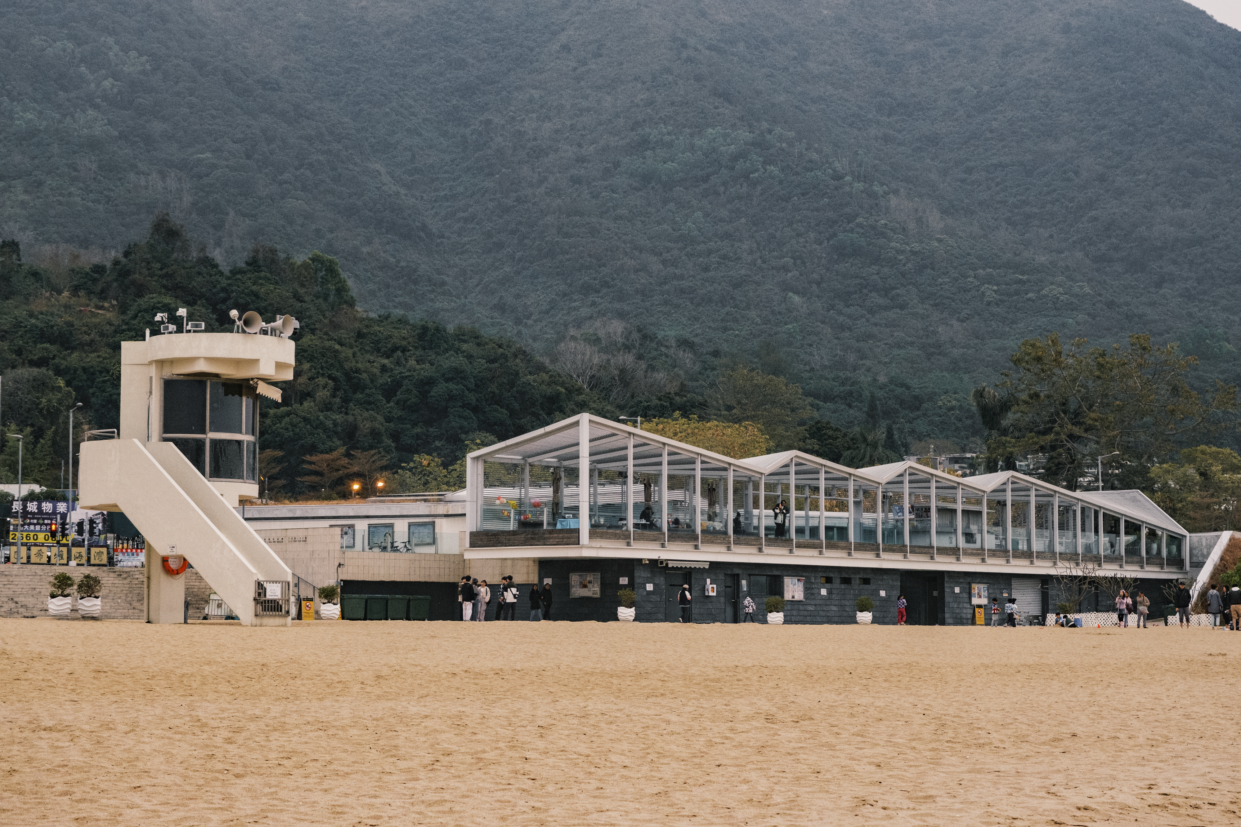 Coastal Convergence: Lifeguard Tower and Glass Pavilion Framing a Mountain Backdrop