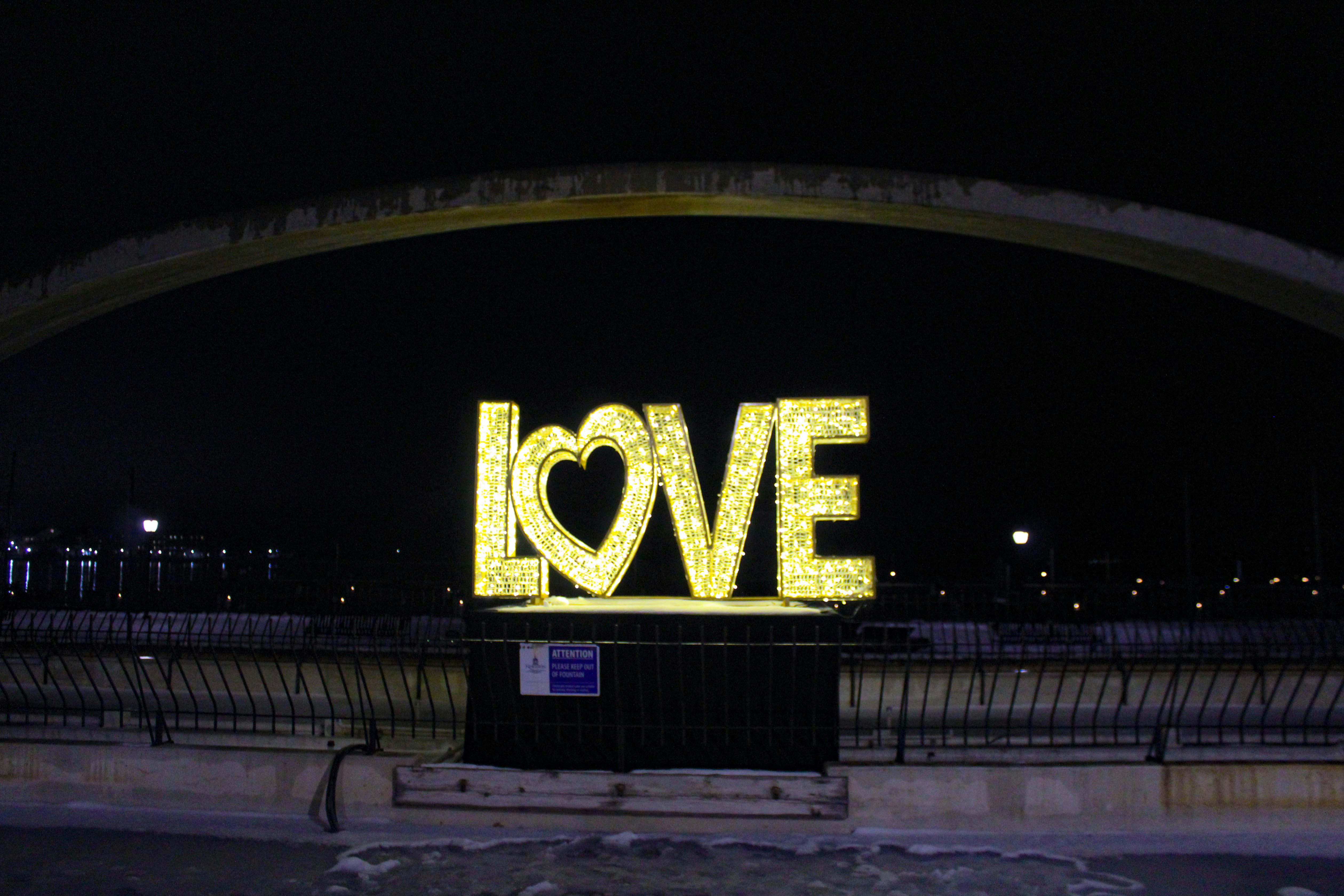 Illuminated 'LOVE' sign glowing against a dark backdrop under an archway.