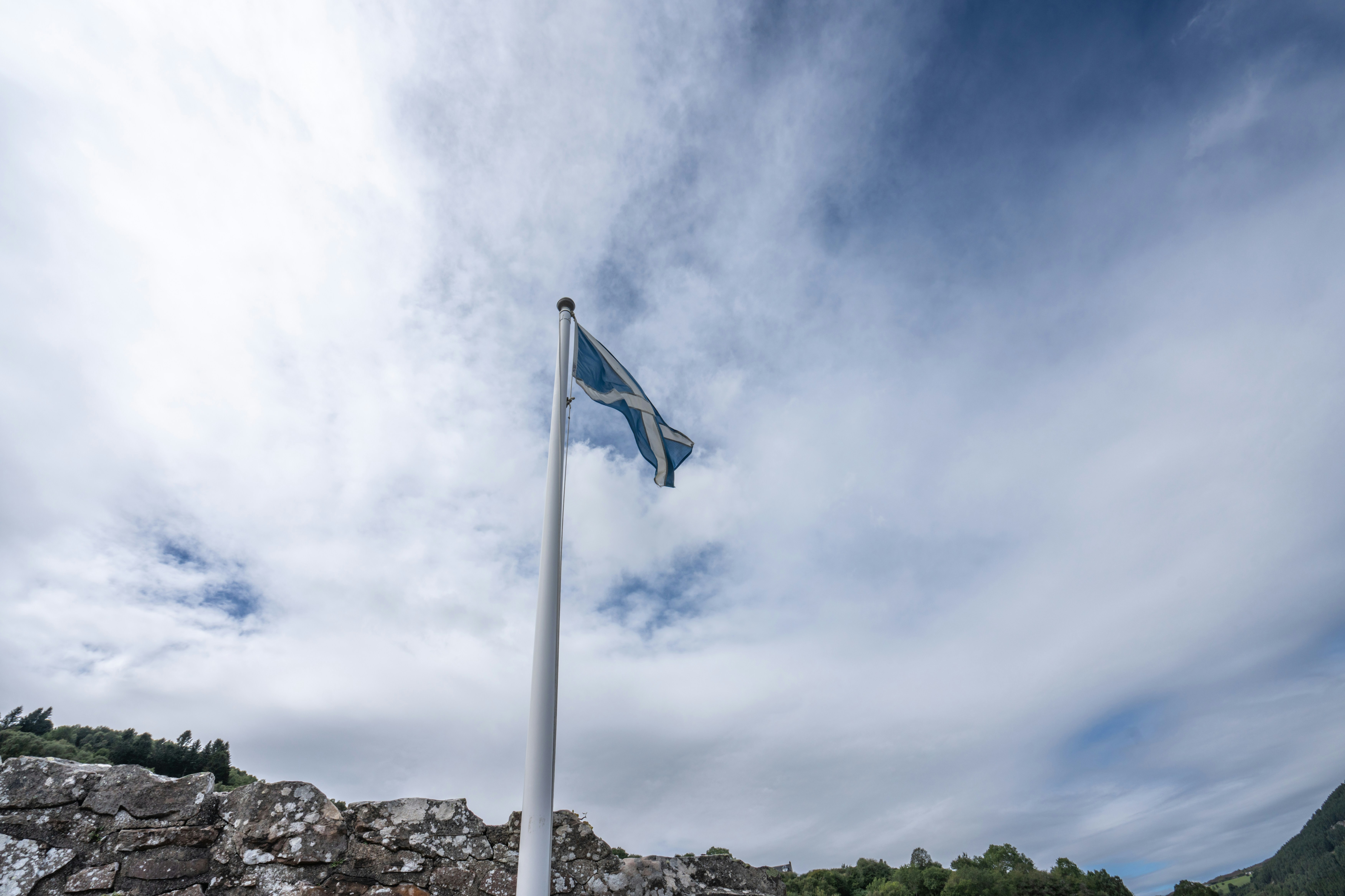 A flag flying high in the sky next to a stone wall photo – Free ...