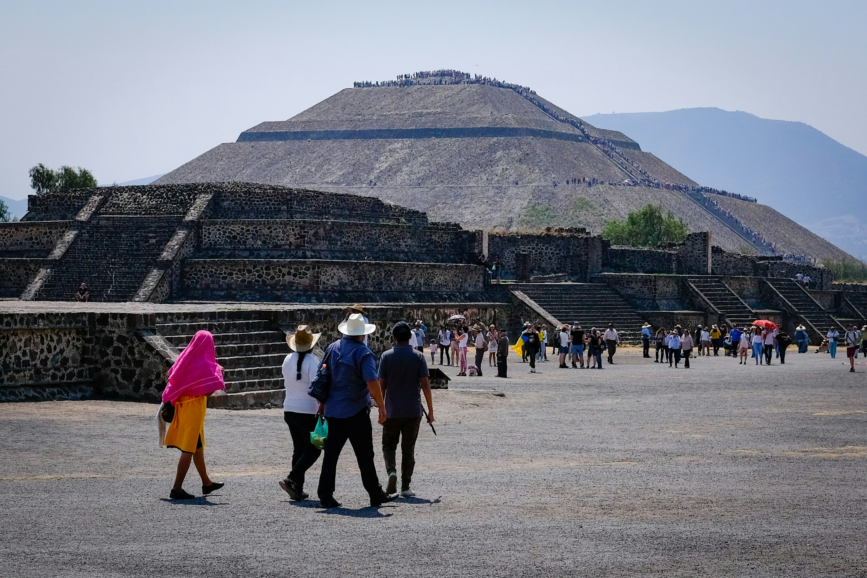 Visitors walk towards the Pyramid of the Sun at Teotihuacan under a clear sky.