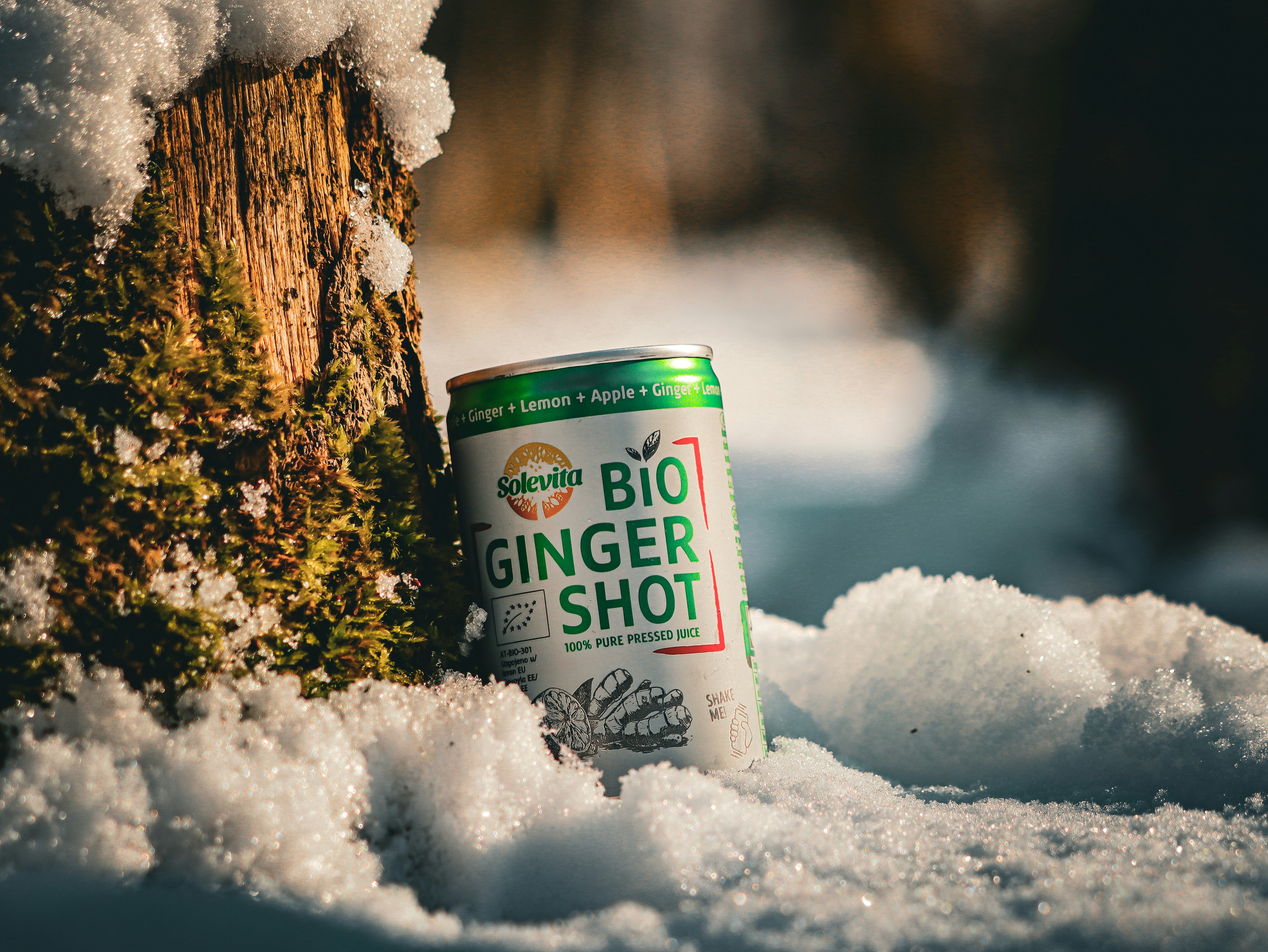 Ginger Shot in Winter Light: A Bright Can Beside a Mossy Snowbank