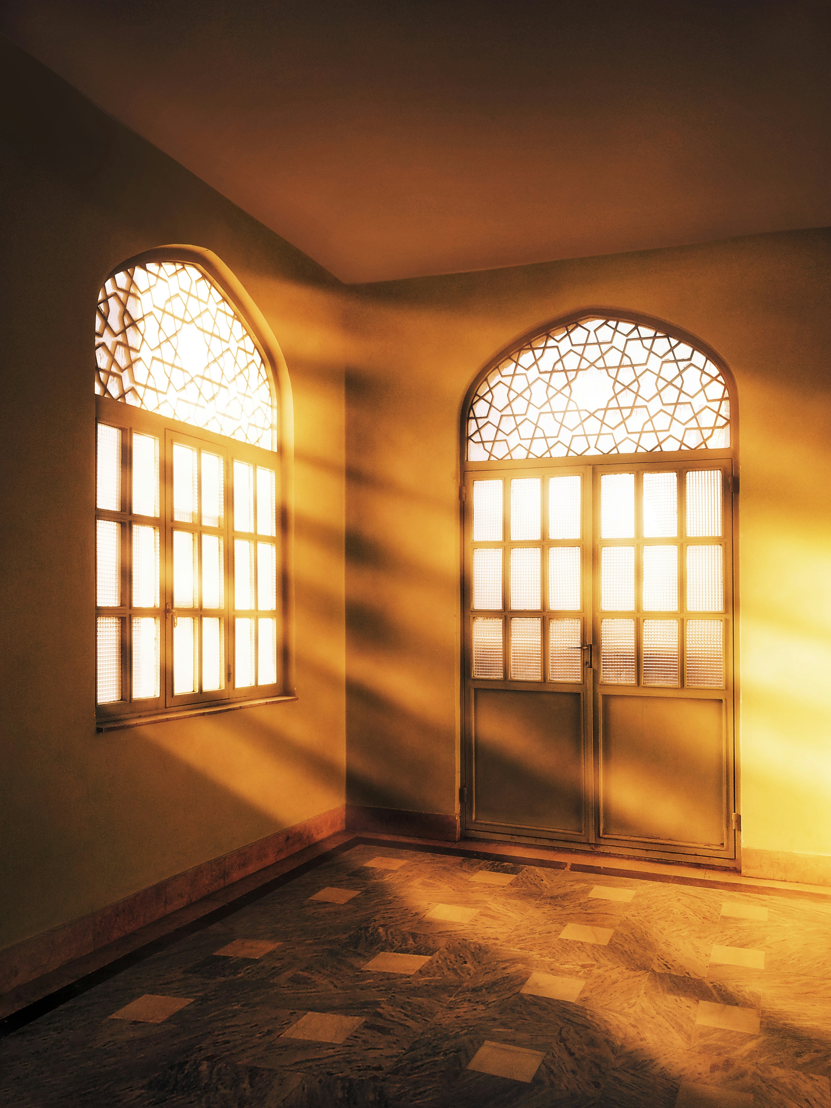 Sunlight streams through intricately designed arched windows, casting warm hues across a softly lit room. The ambiance evokes a sense of tranquility and historic charm.
