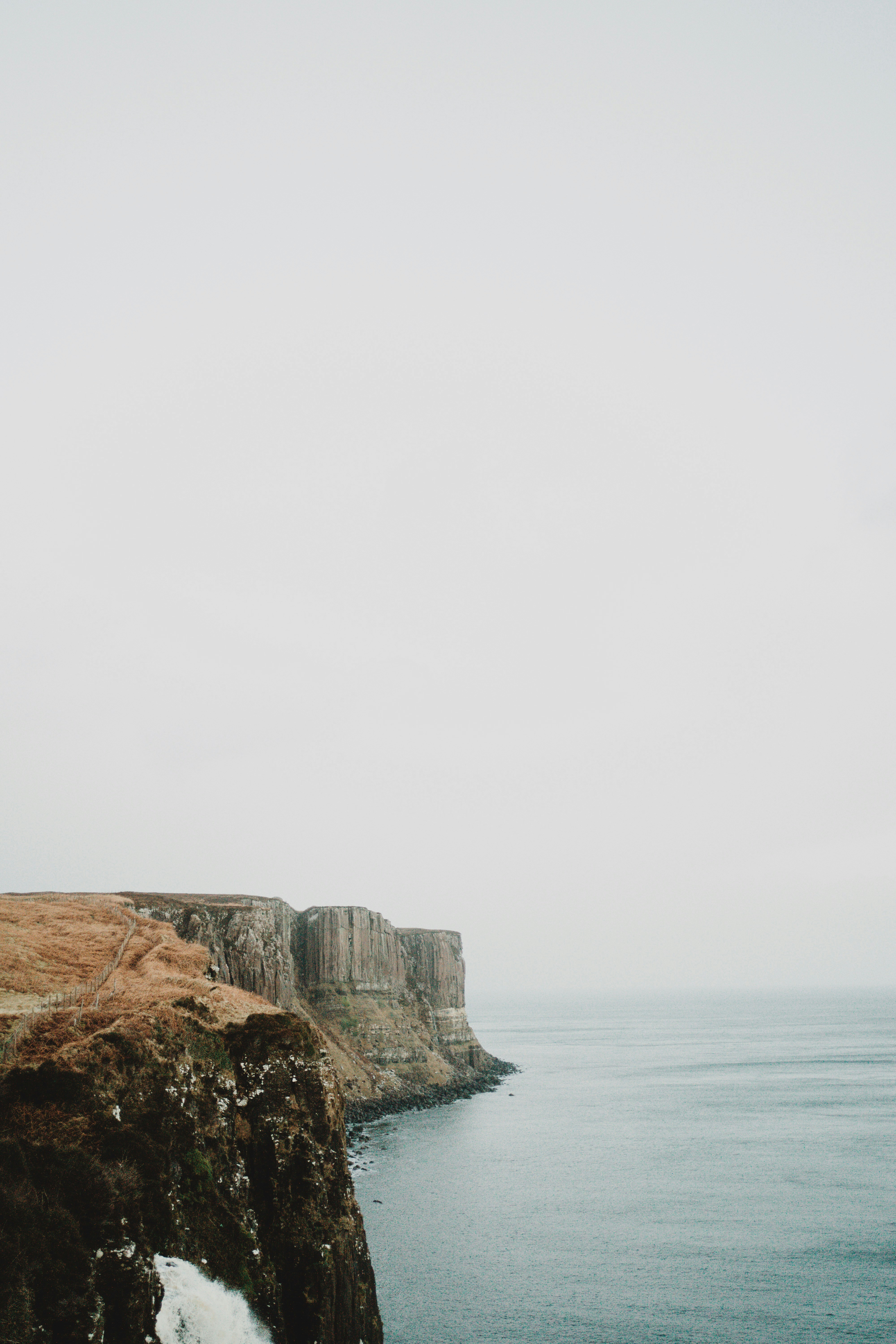 A person standing on top of a cliff next to the ocean photo – Free ...
