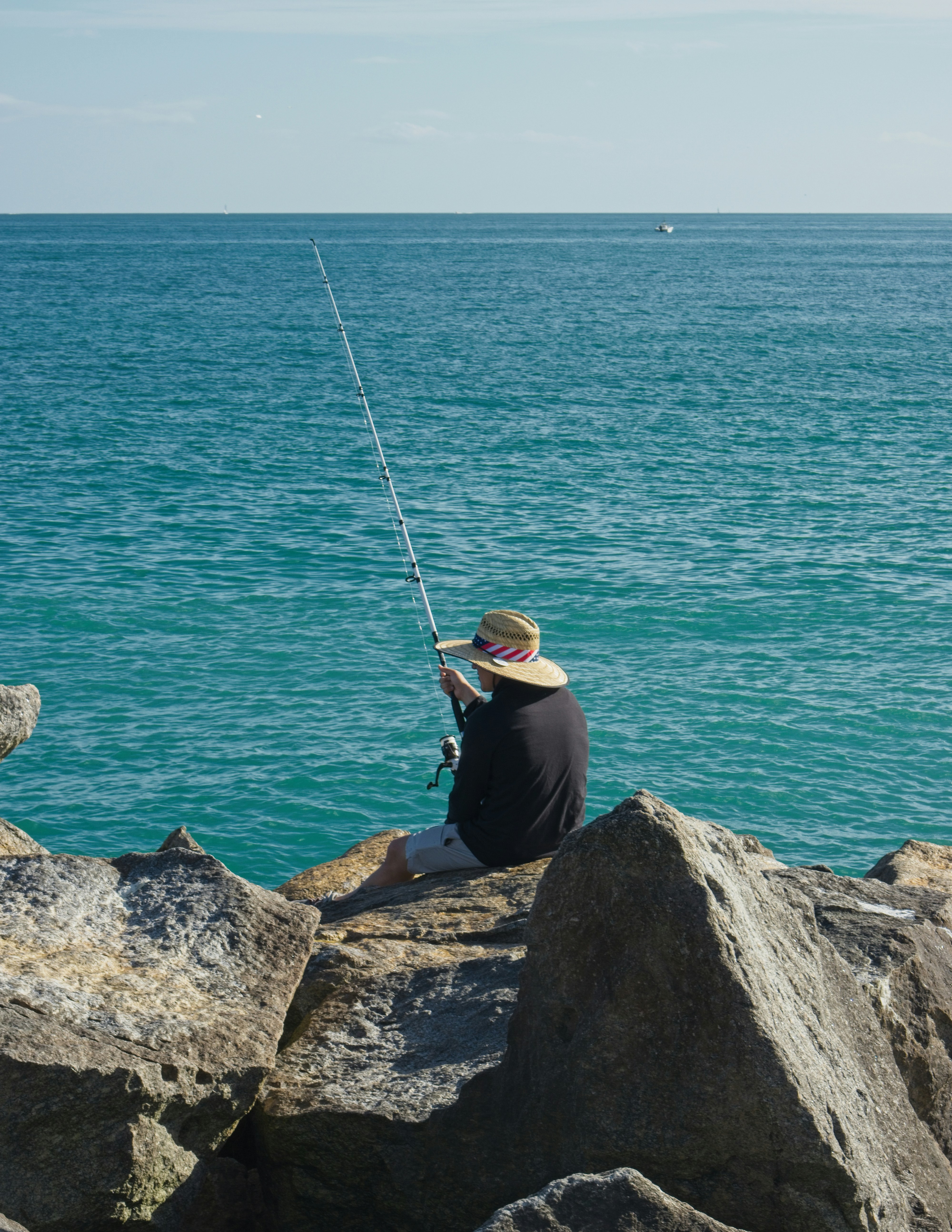 Foto Un hombre sentado en una roca pescando en el océano – Imagen Azul ...