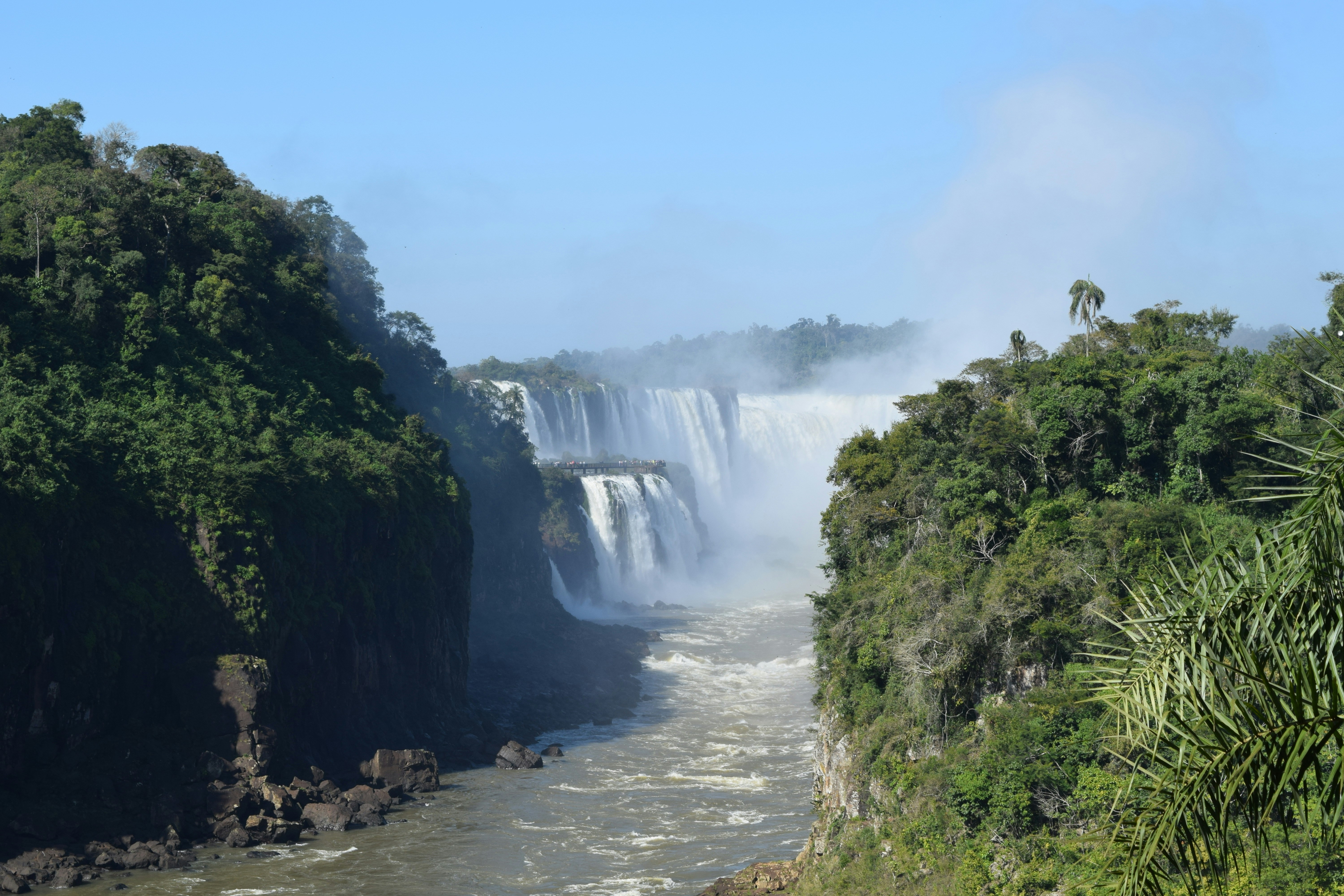 Towering waterfall surrounded by lush green forest under a clear blue sky.