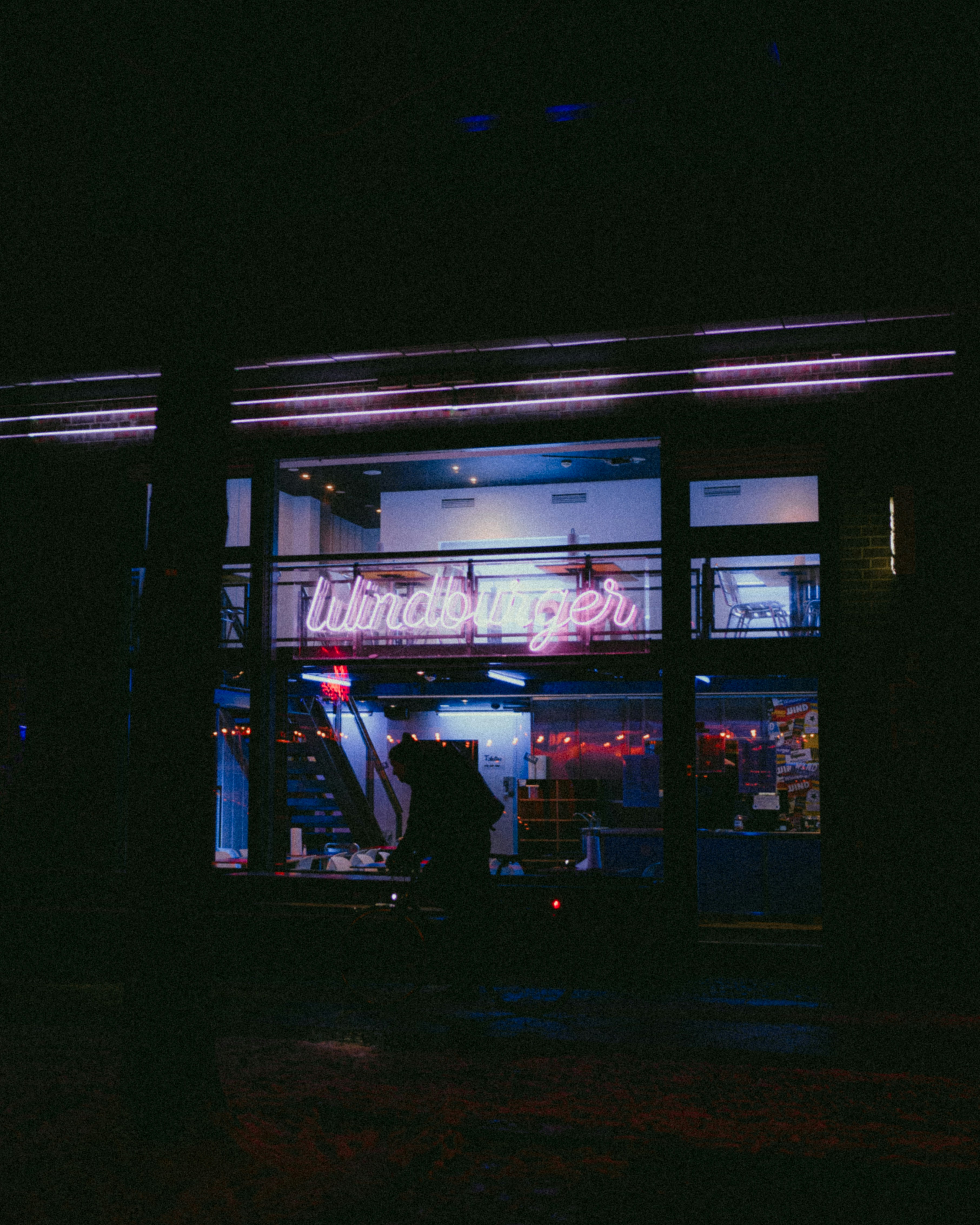 Illuminated restaurant exterior featuring a vibrant neon sign, with a silhouette of a person in the foreground. The scene captures the essence of urban nightlife.
