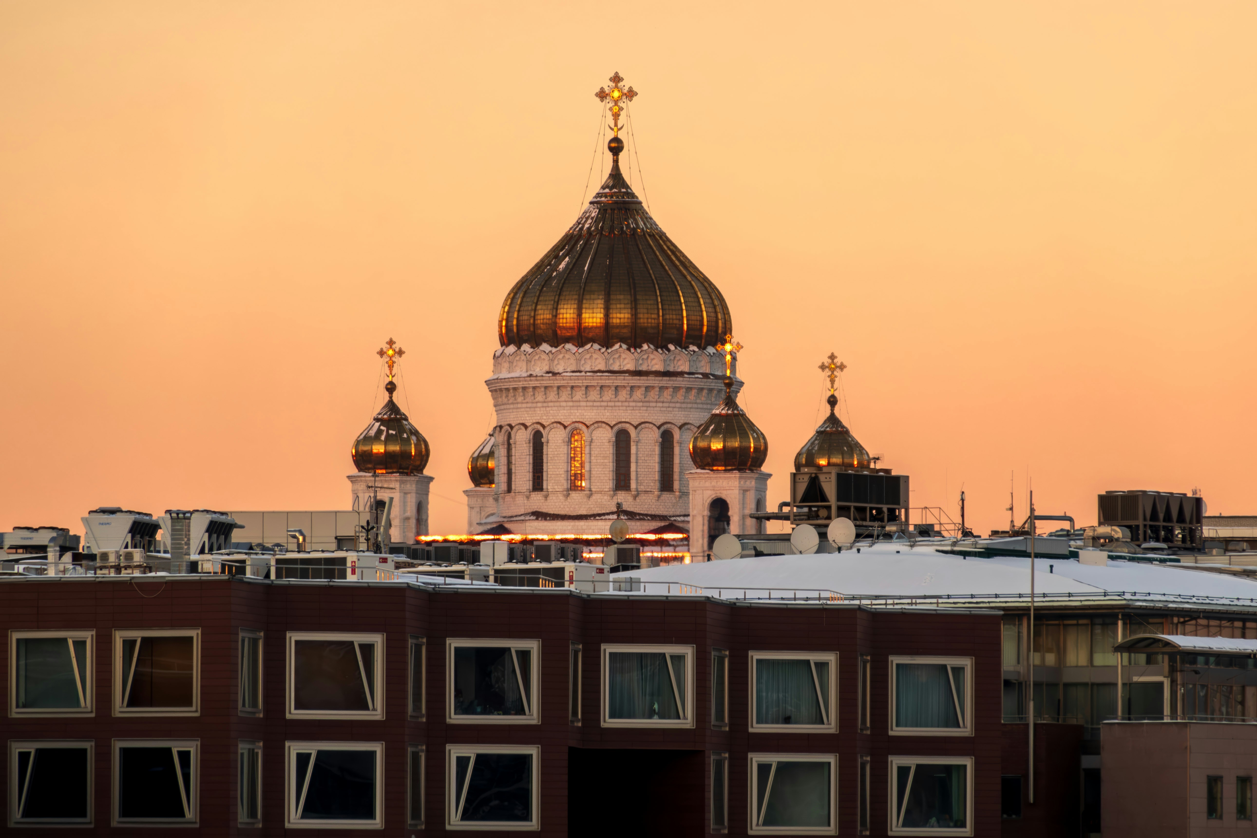 Golden domes of a cathedral shine against a warm evening sky over modern rooftops.