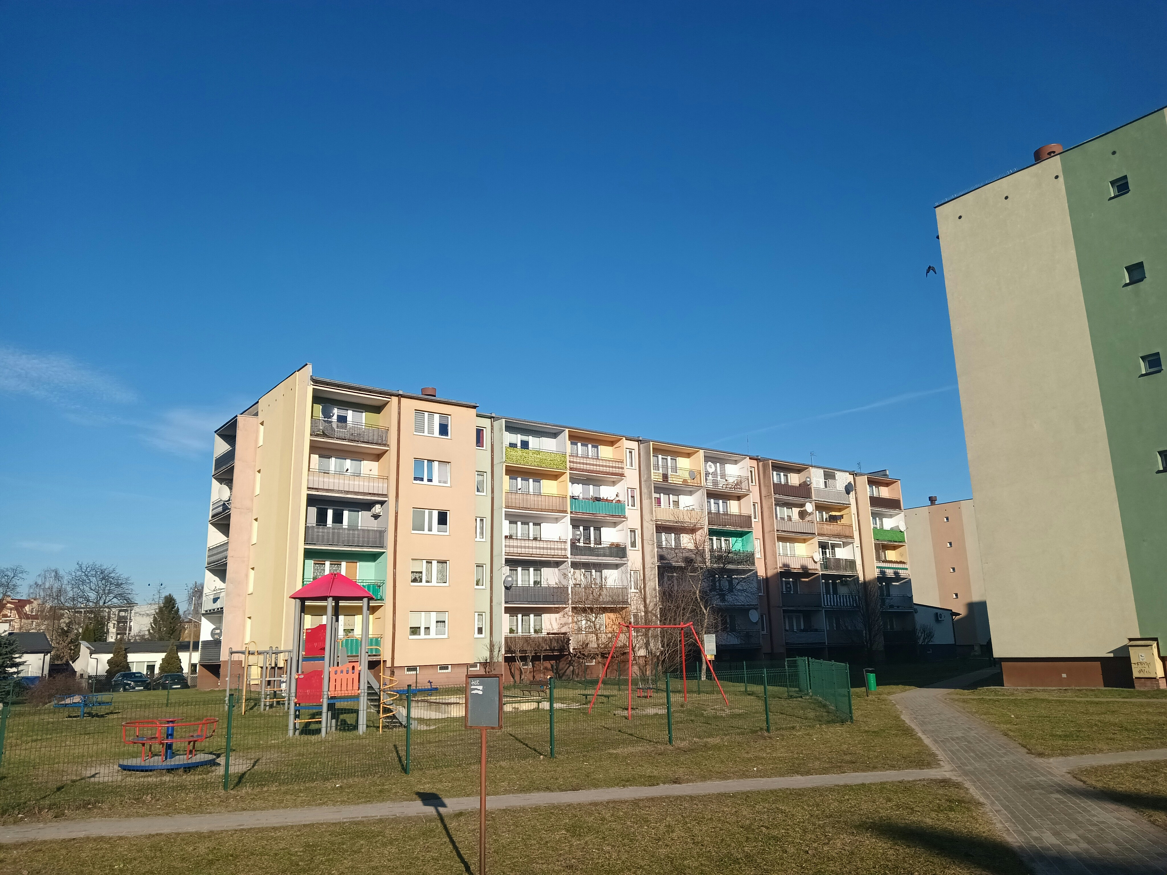 Pastel apartment block with a playground in the foreground during daytime.