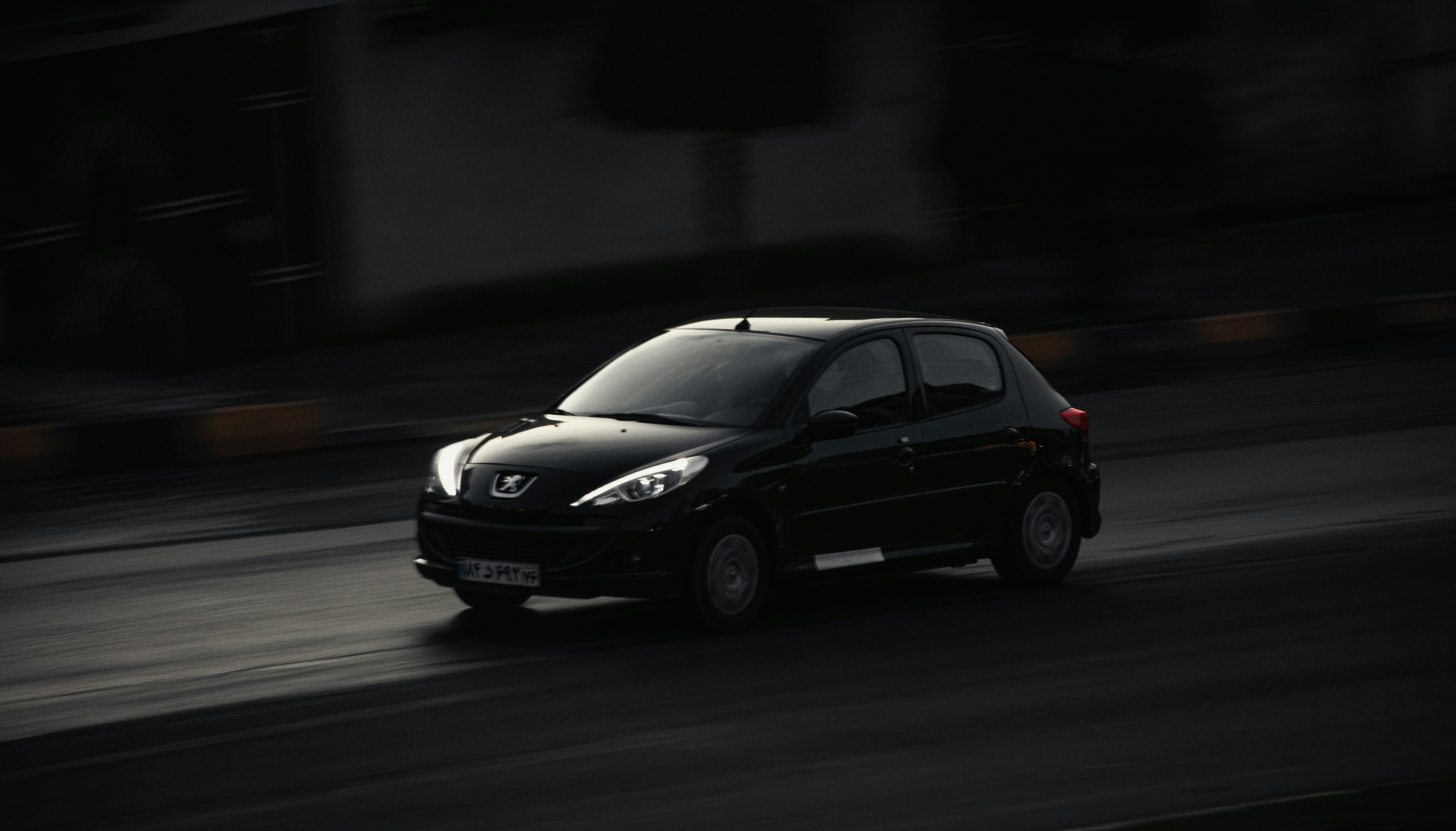 Nocturnal Dash: A Black Hatchback Slices Through Dim Streetlight