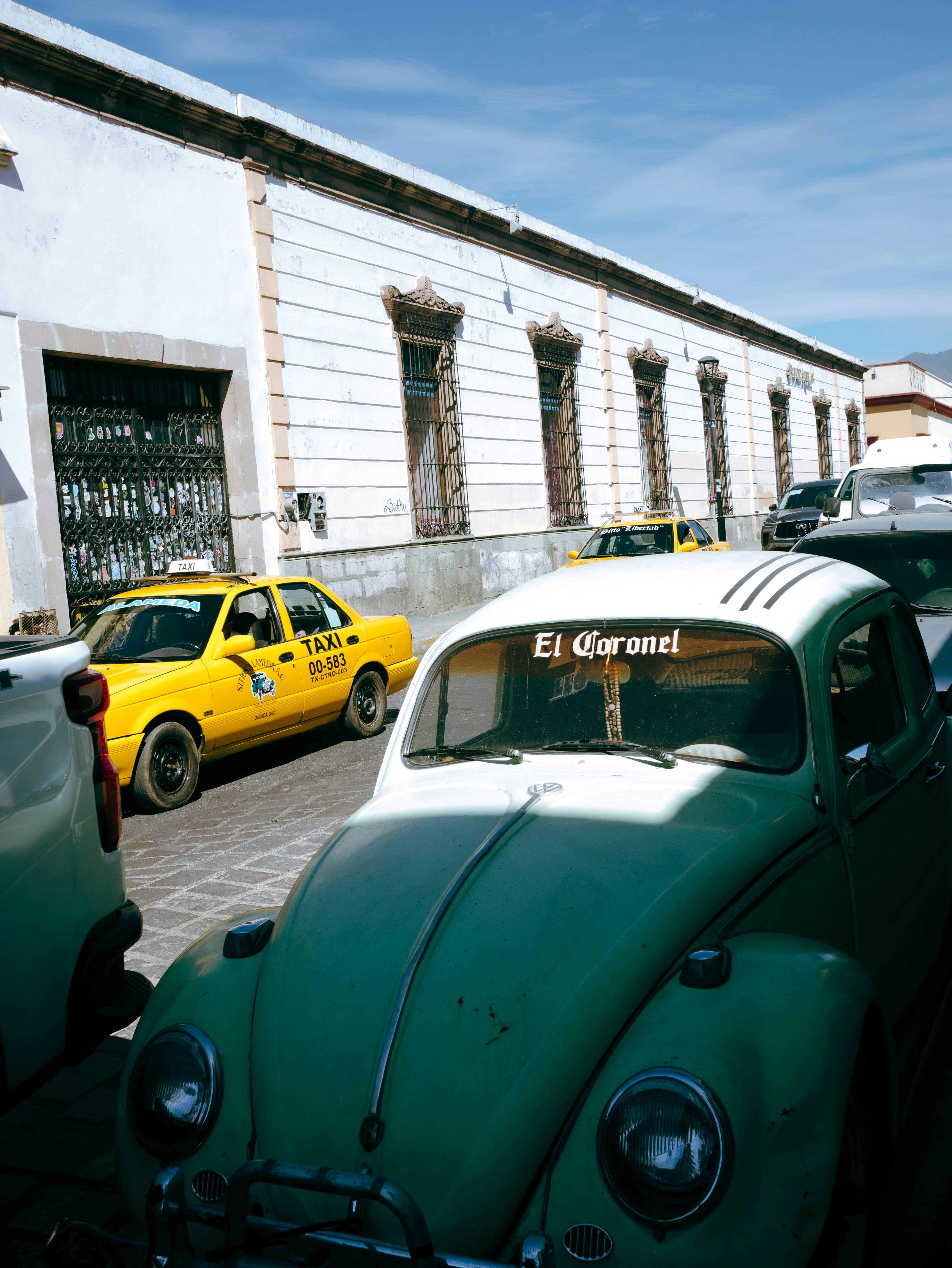 Classic VW Beetle and a row of yellow taxis line a sunlit colonial street.