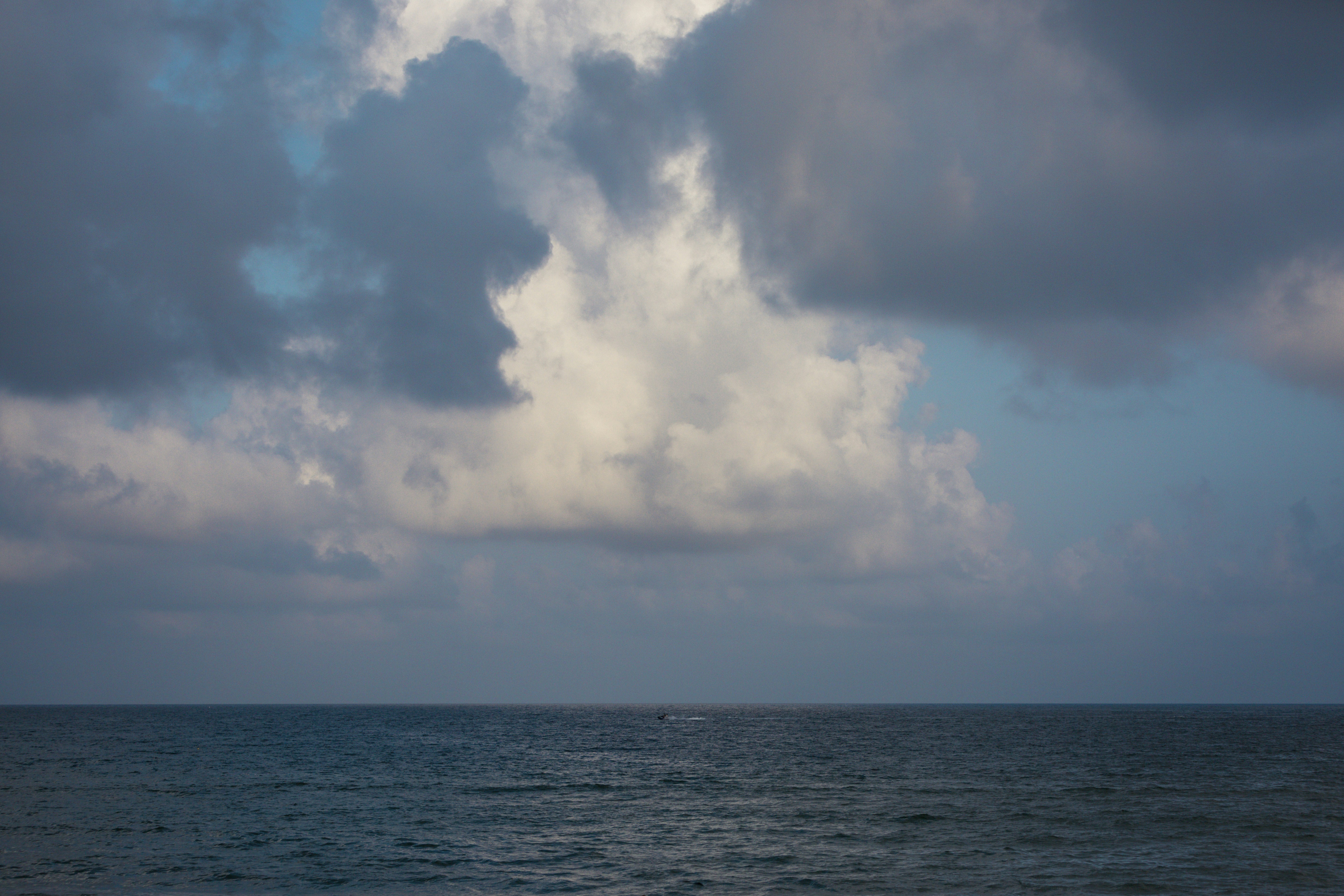 Dramatic clouds form above a calm ocean at dusk.