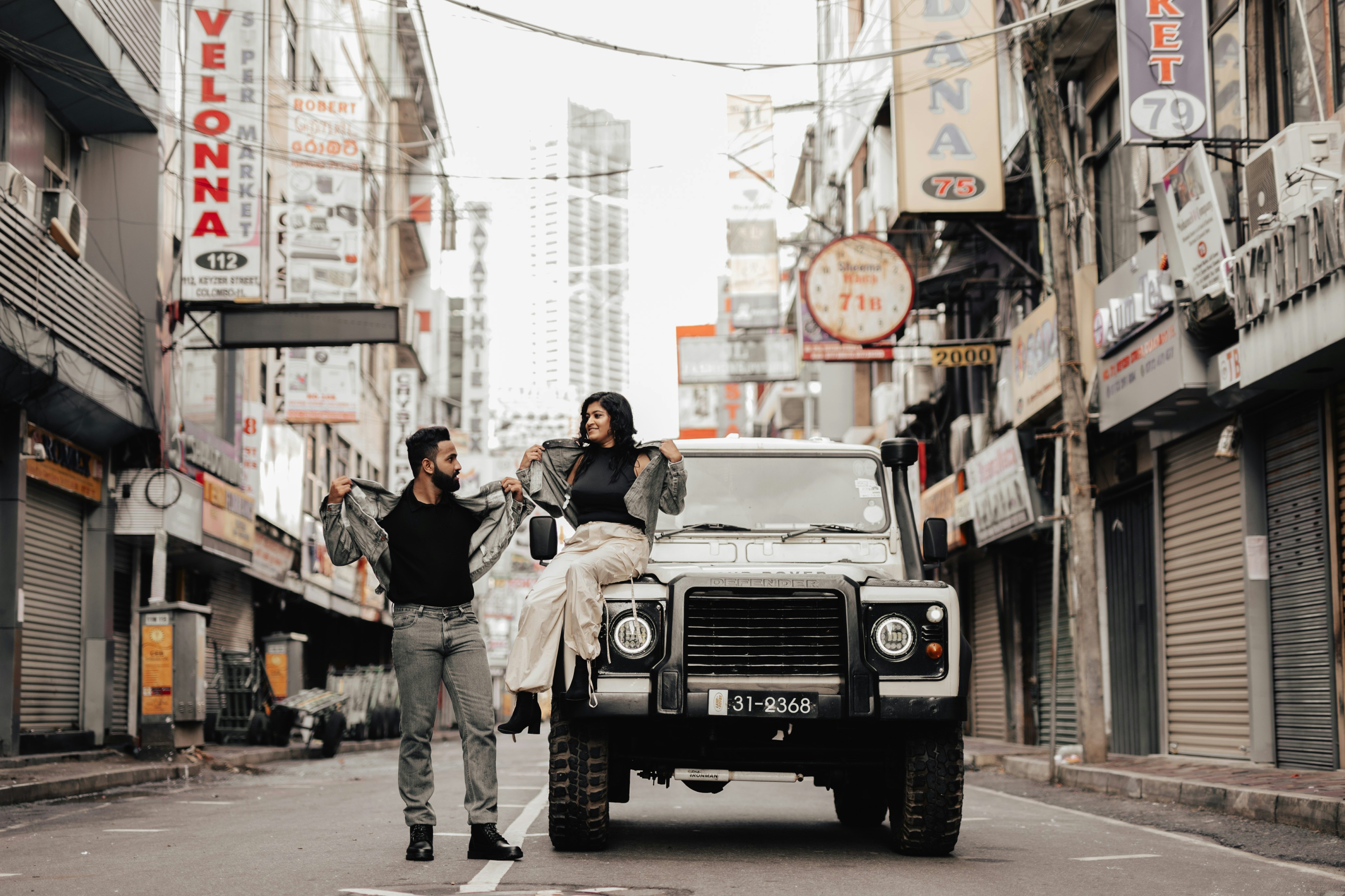Neon Street Waltz: A Couple Framed by a Weathered SUV Amid a Corridor of Signs