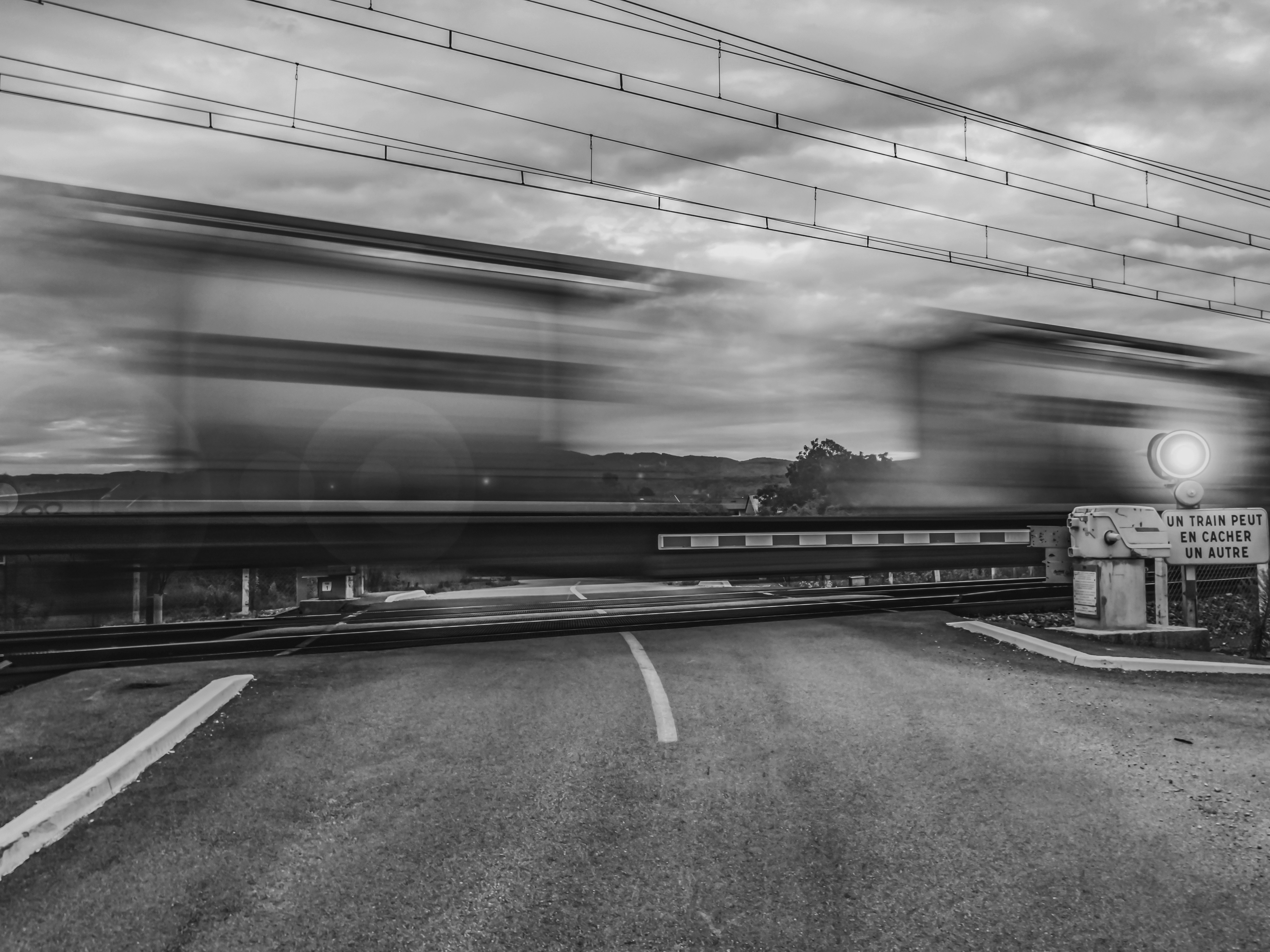A blurred train crossing a rural road, emphasizing motion and the fleeting nature of travel in a monochromatic setting.