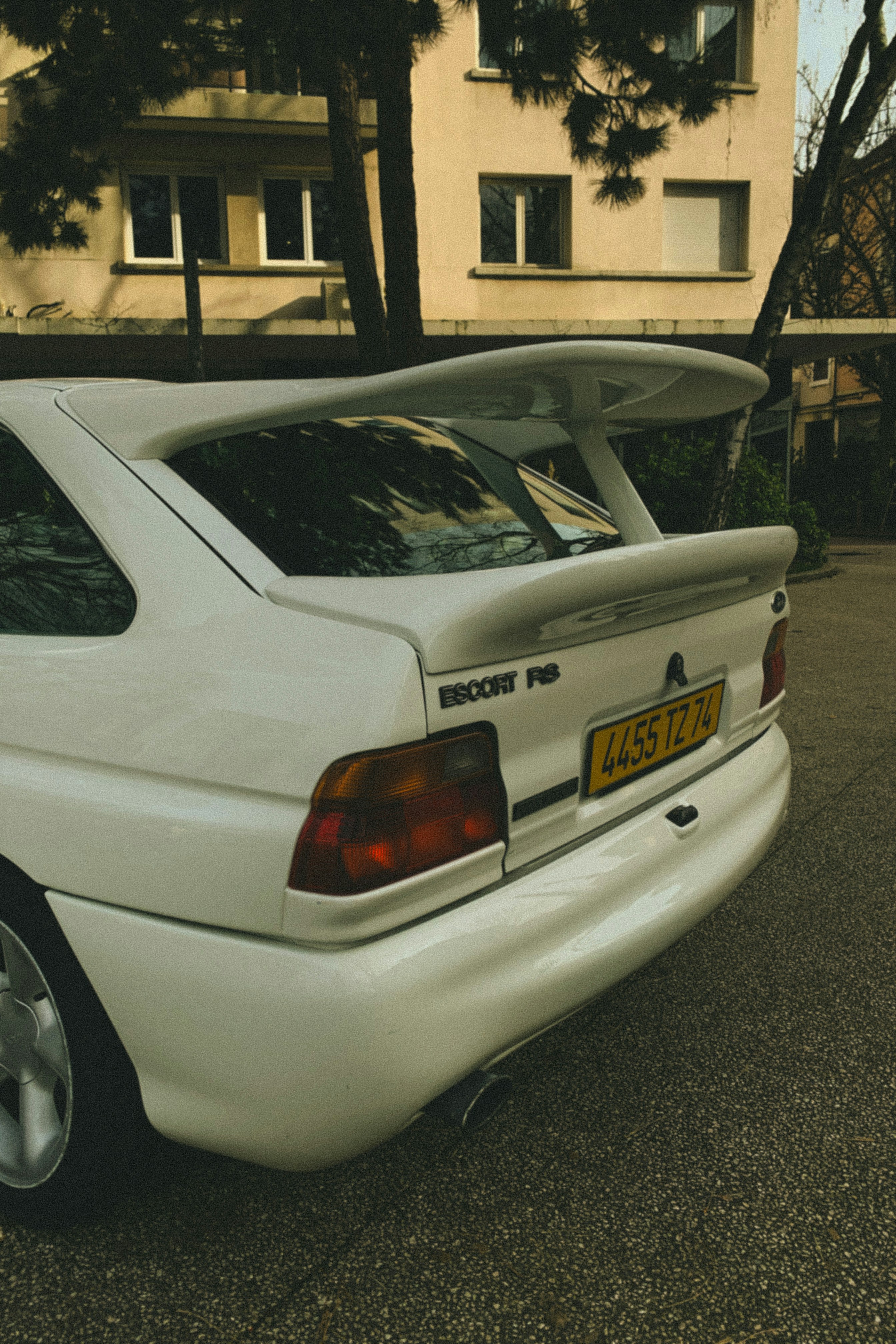 Rear view of a white Ford Escort RS parked in an urban setting, showcasing its iconic design and sporty rear wing.