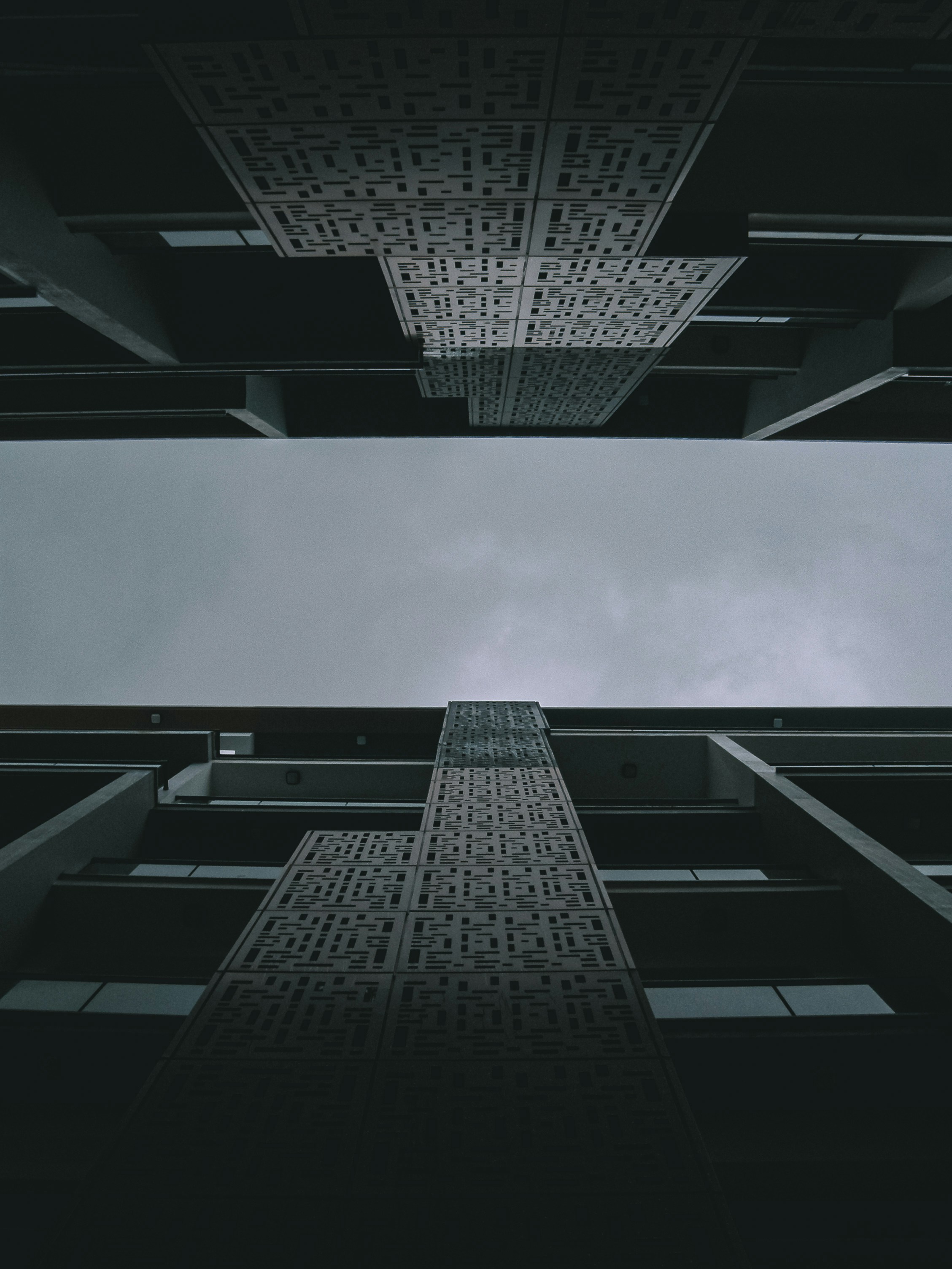 Architectural photograph showing two tall buildings framing a narrow sky gap with a perforated central column, emphasizing depth and symmetry.