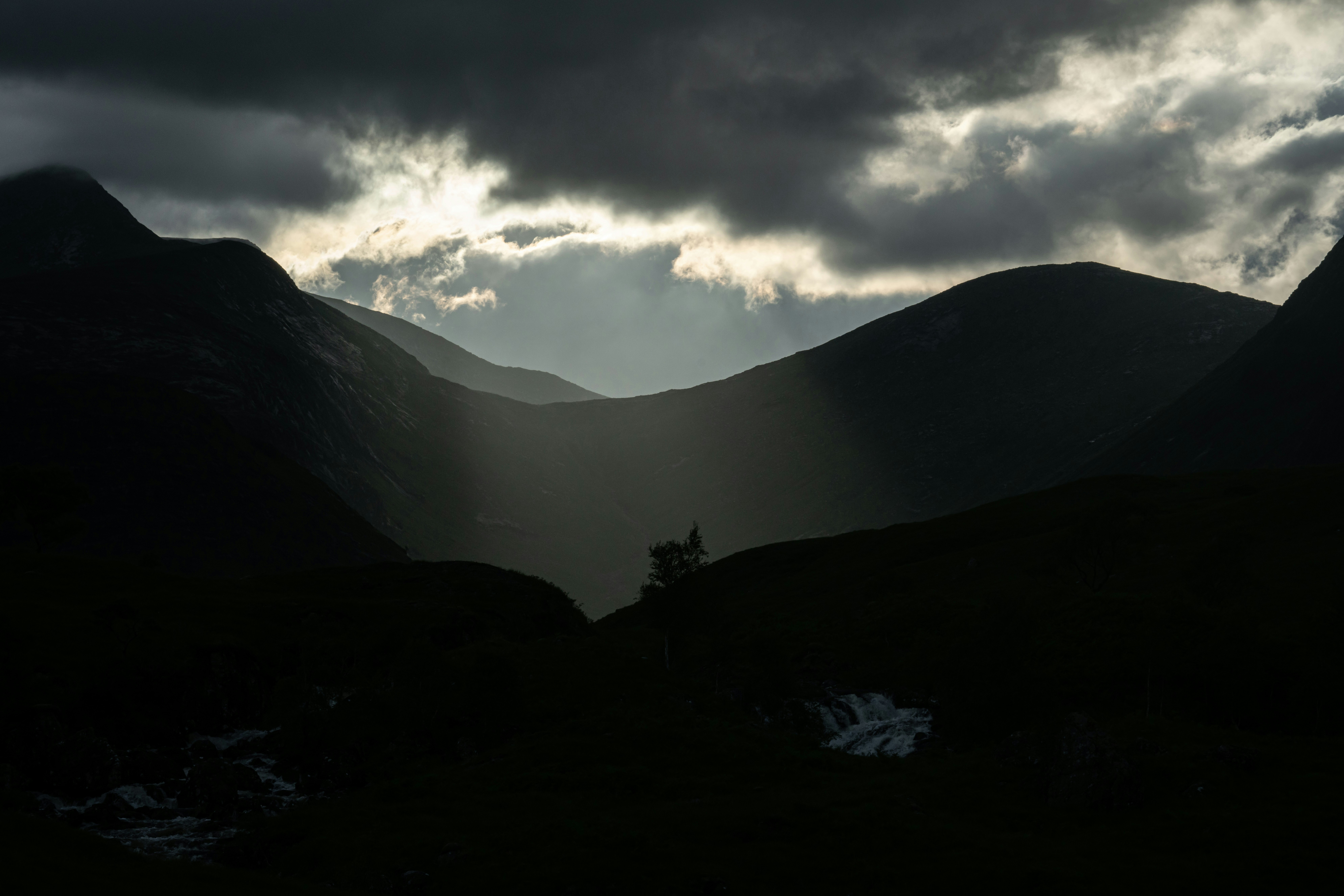 Sunlight pierces through clouds over shadowy mountain silhouettes.