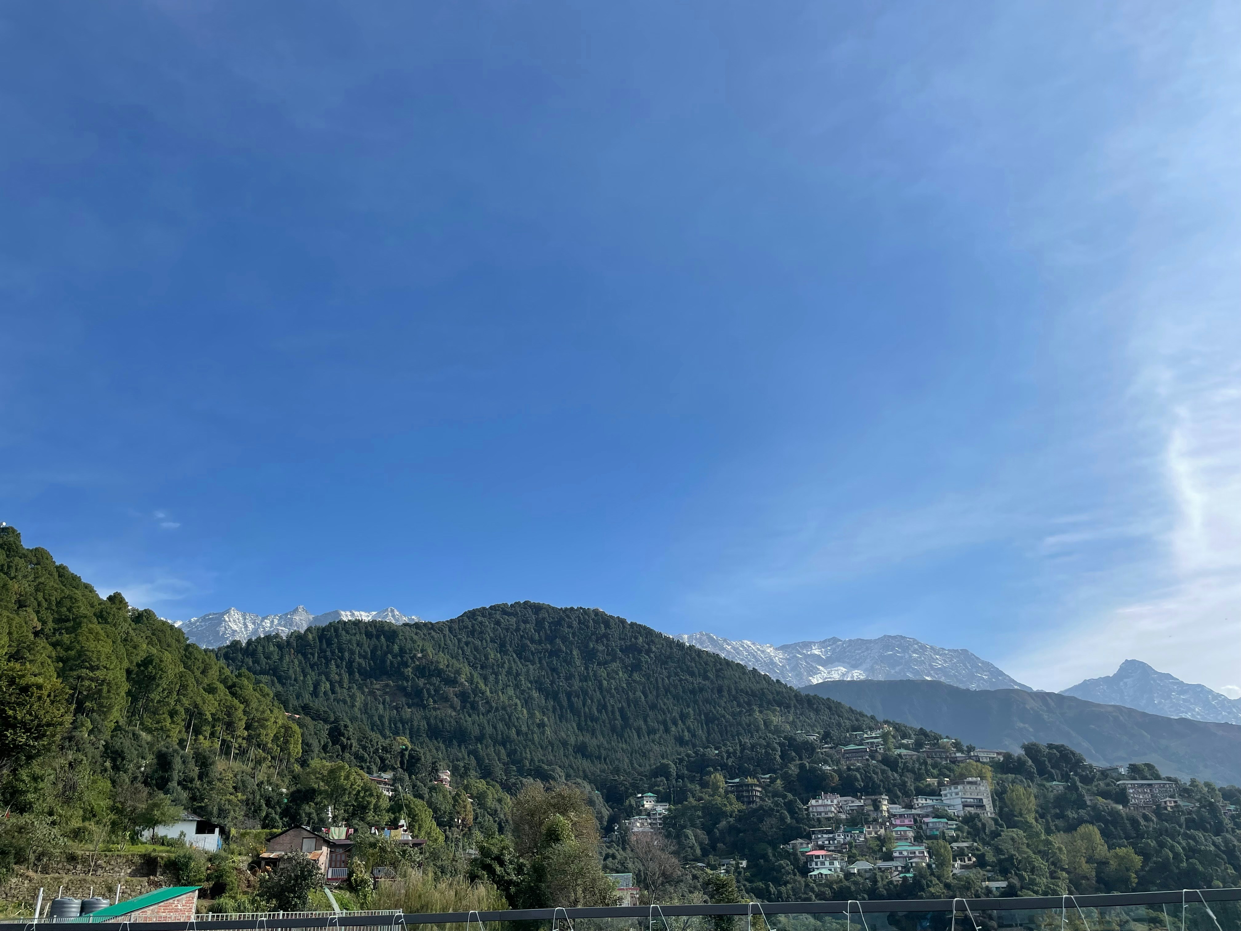 Expansive blue sky over lush green hills and distant snow-capped peaks in McLeodganj.