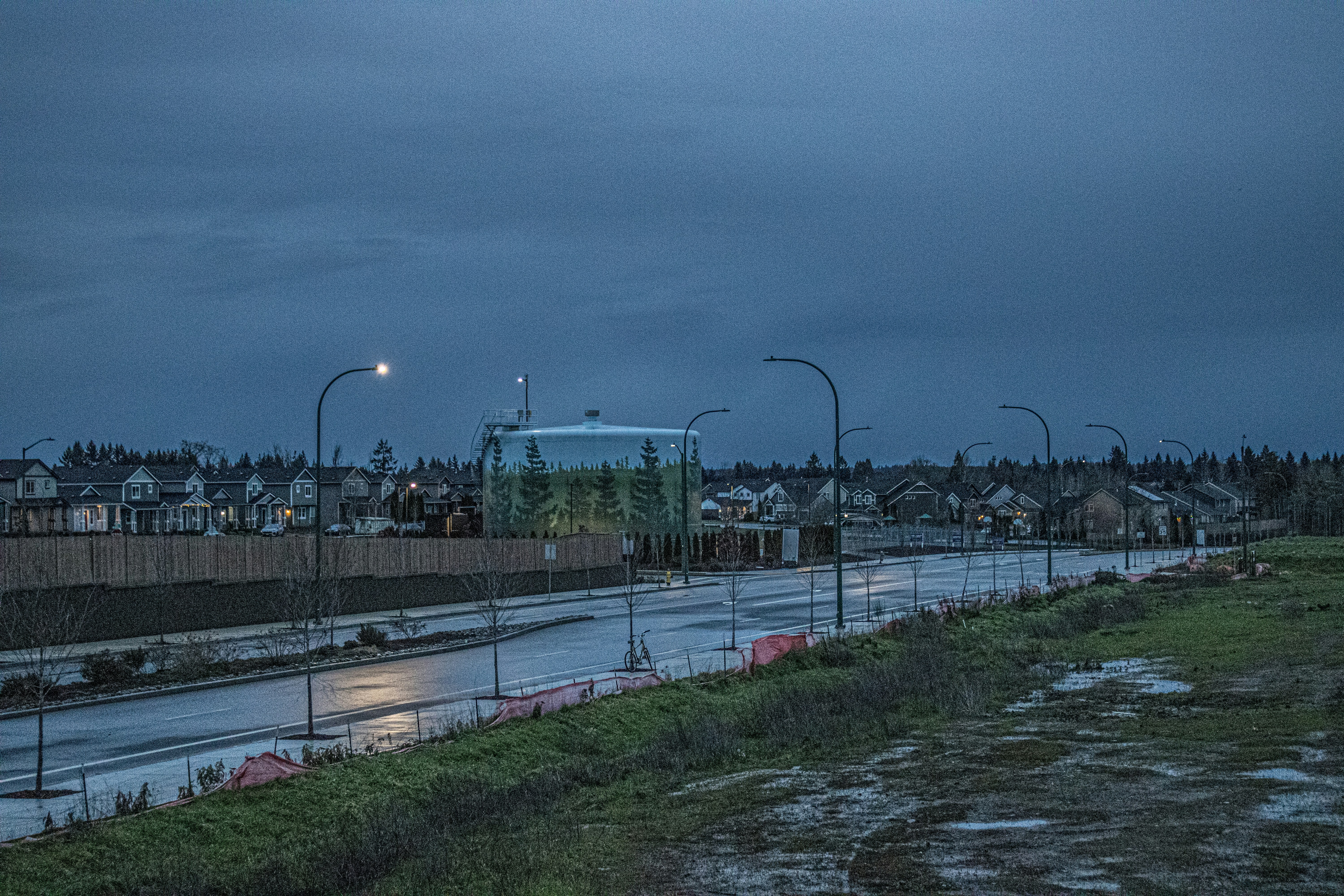 Dusk on the Wet Suburban Edge: Streetlights, Reflections, and a Quiet Row of Homes