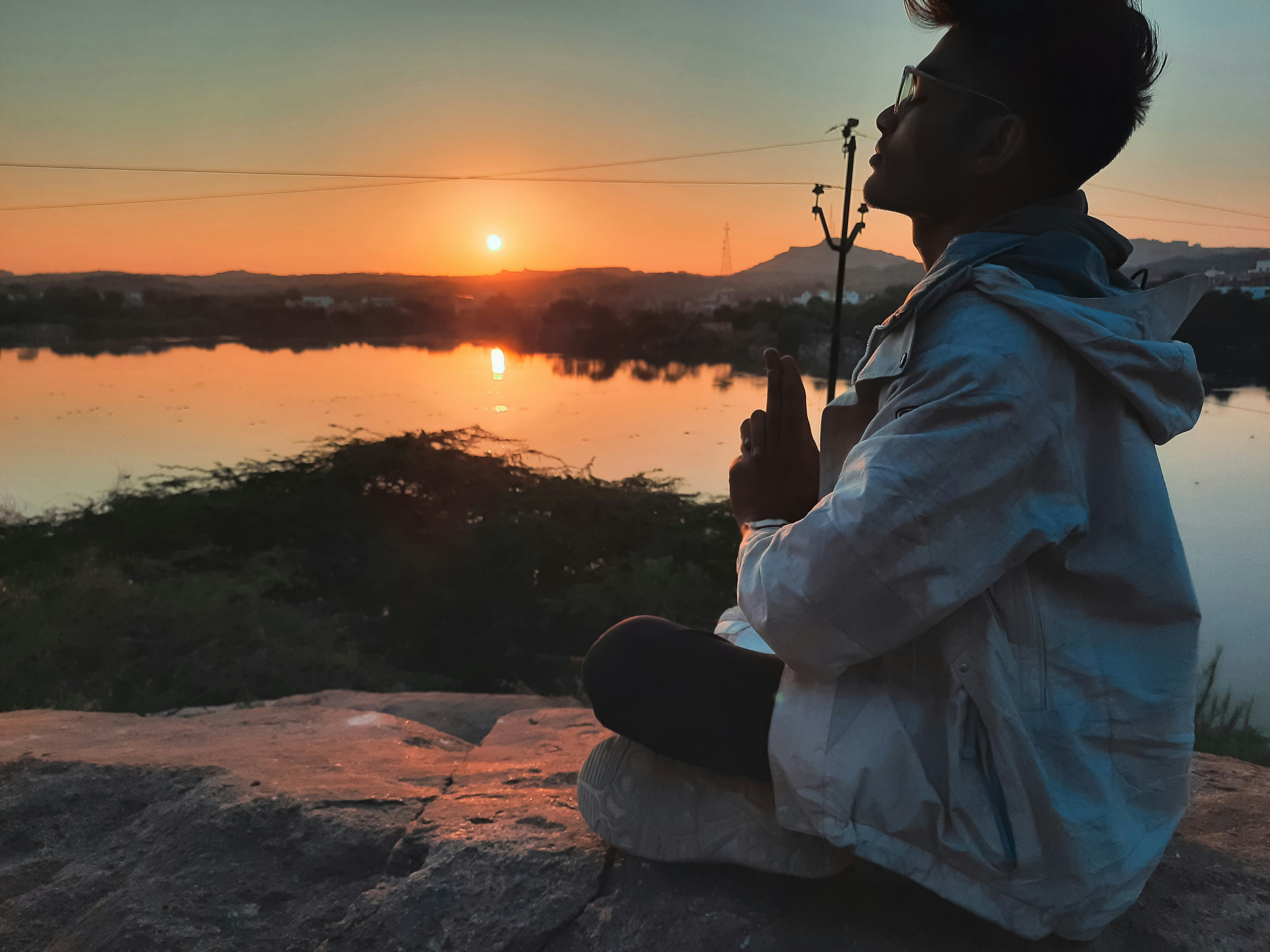 Person meditating by a lake at sunset with vibrant colors in the sky.