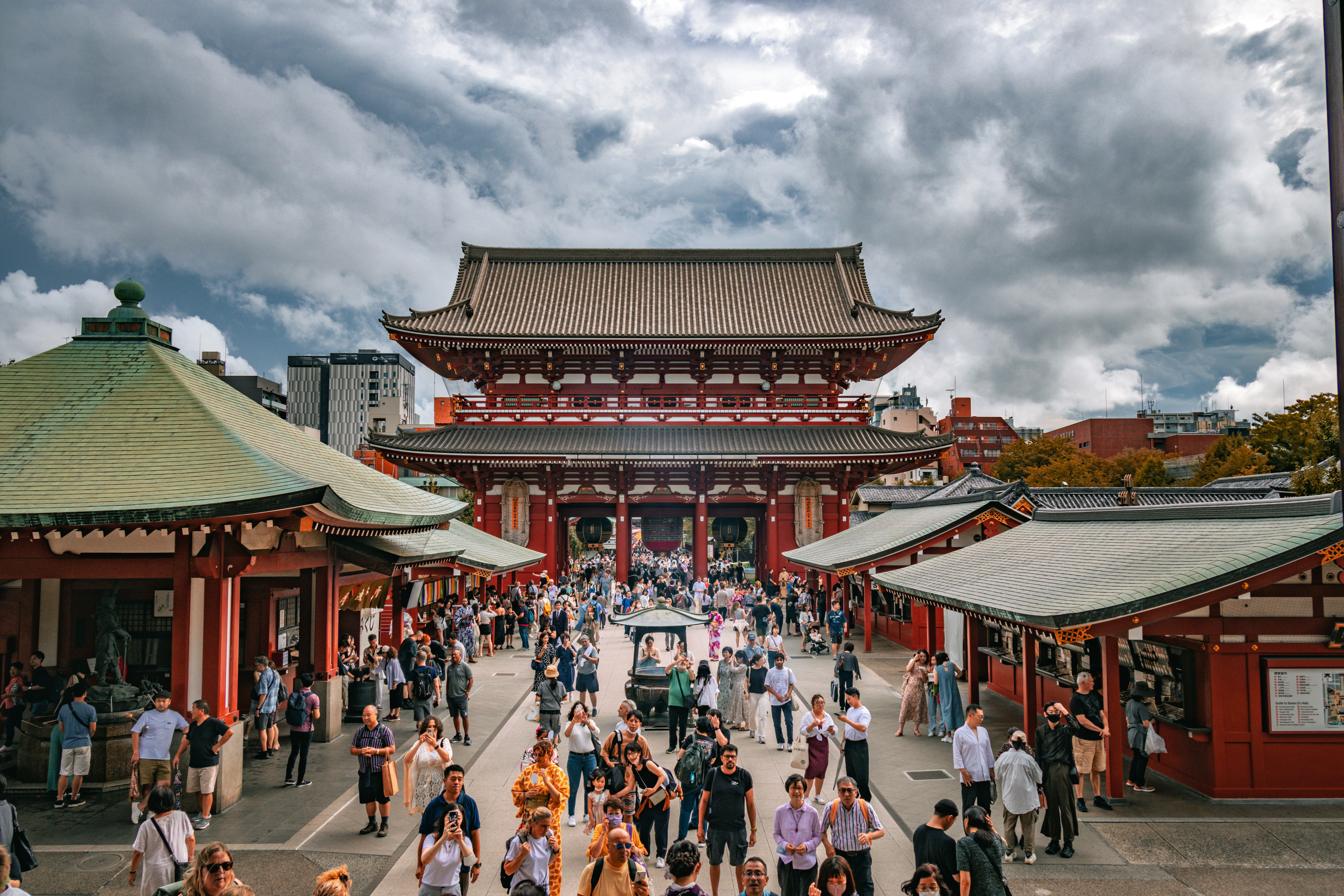 Crowd of visitors exploring the historic Senso-ji Temple in Asakusa, Tokyo, framed by vibrant architecture and a dynamic sky.