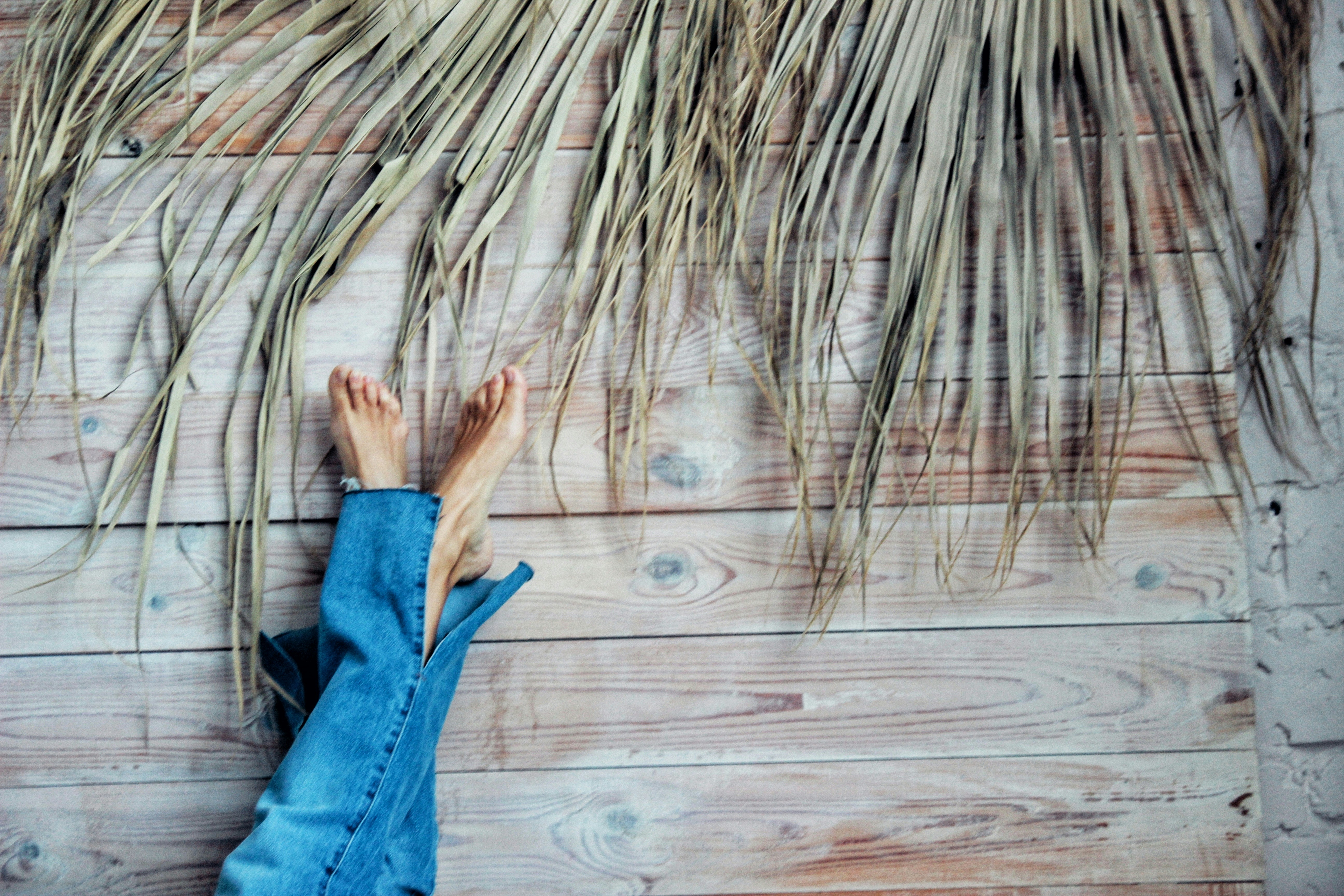 Bare feet dangling from a wooden wall adorned with dry palm leaves.