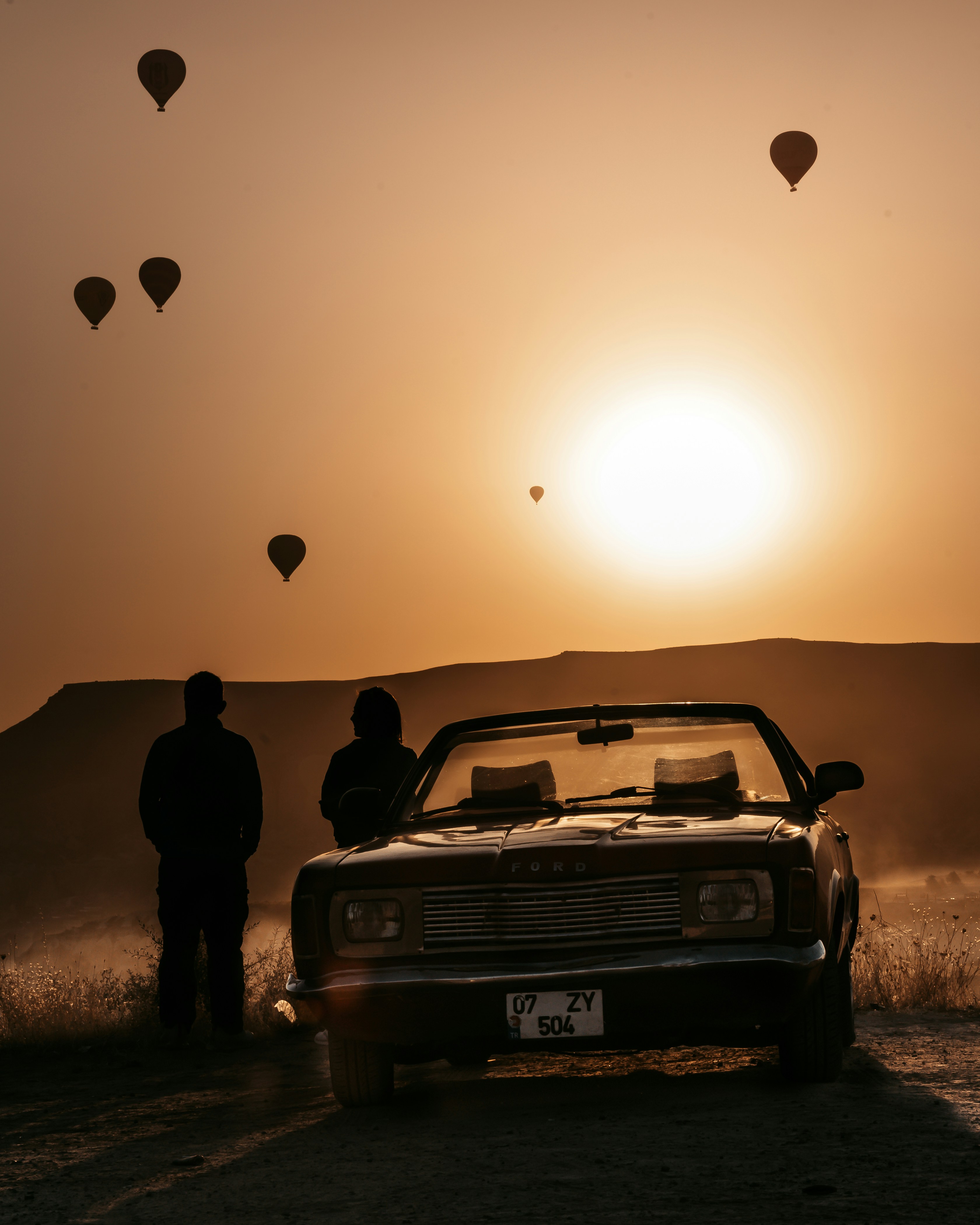 Burnt-Orange Horizon: Balloons Drifting Over a Desert Convertible Silhouette