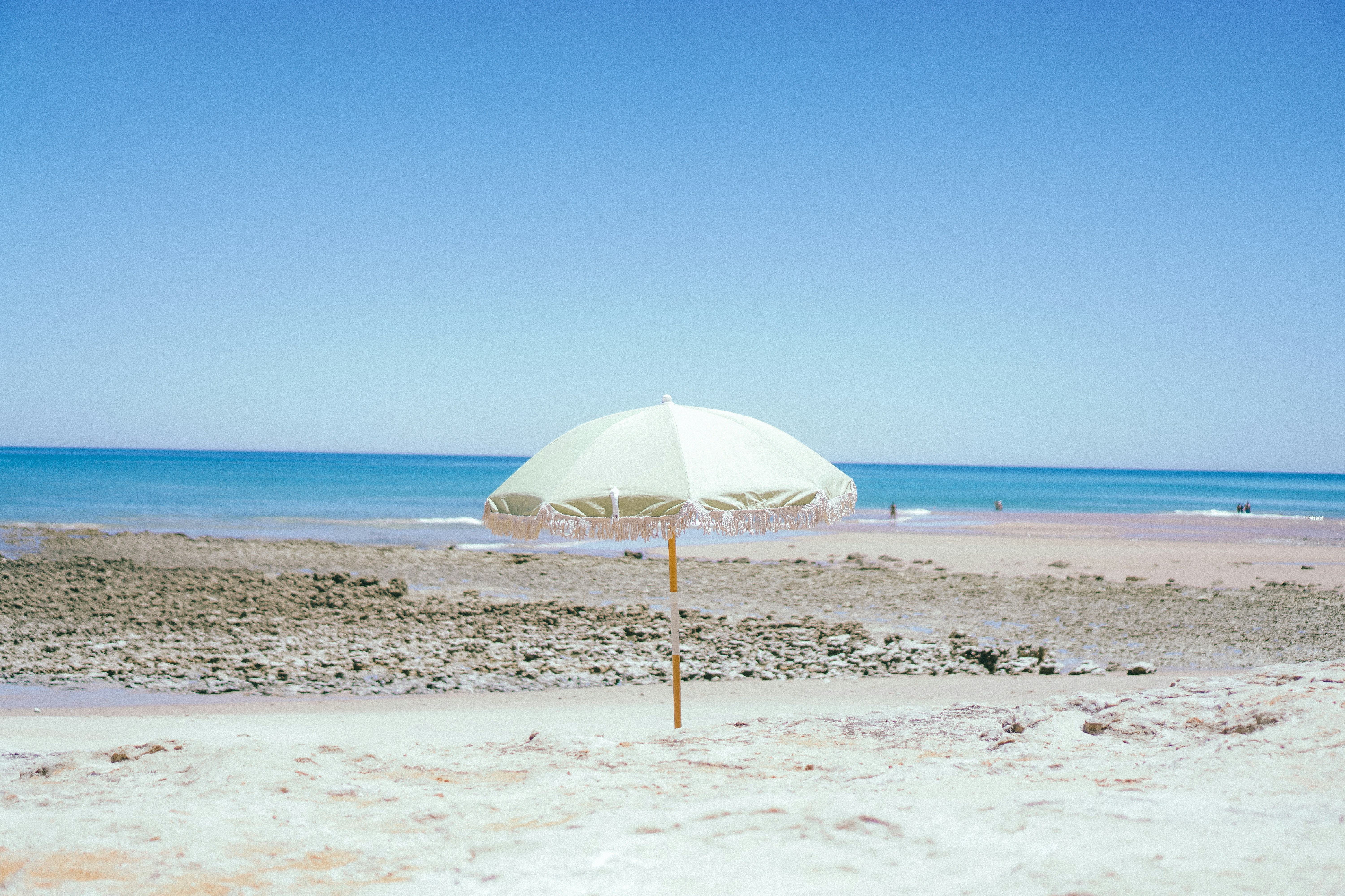 Una sombrilla blanca sentada en la parte superior de una playa de arena ...