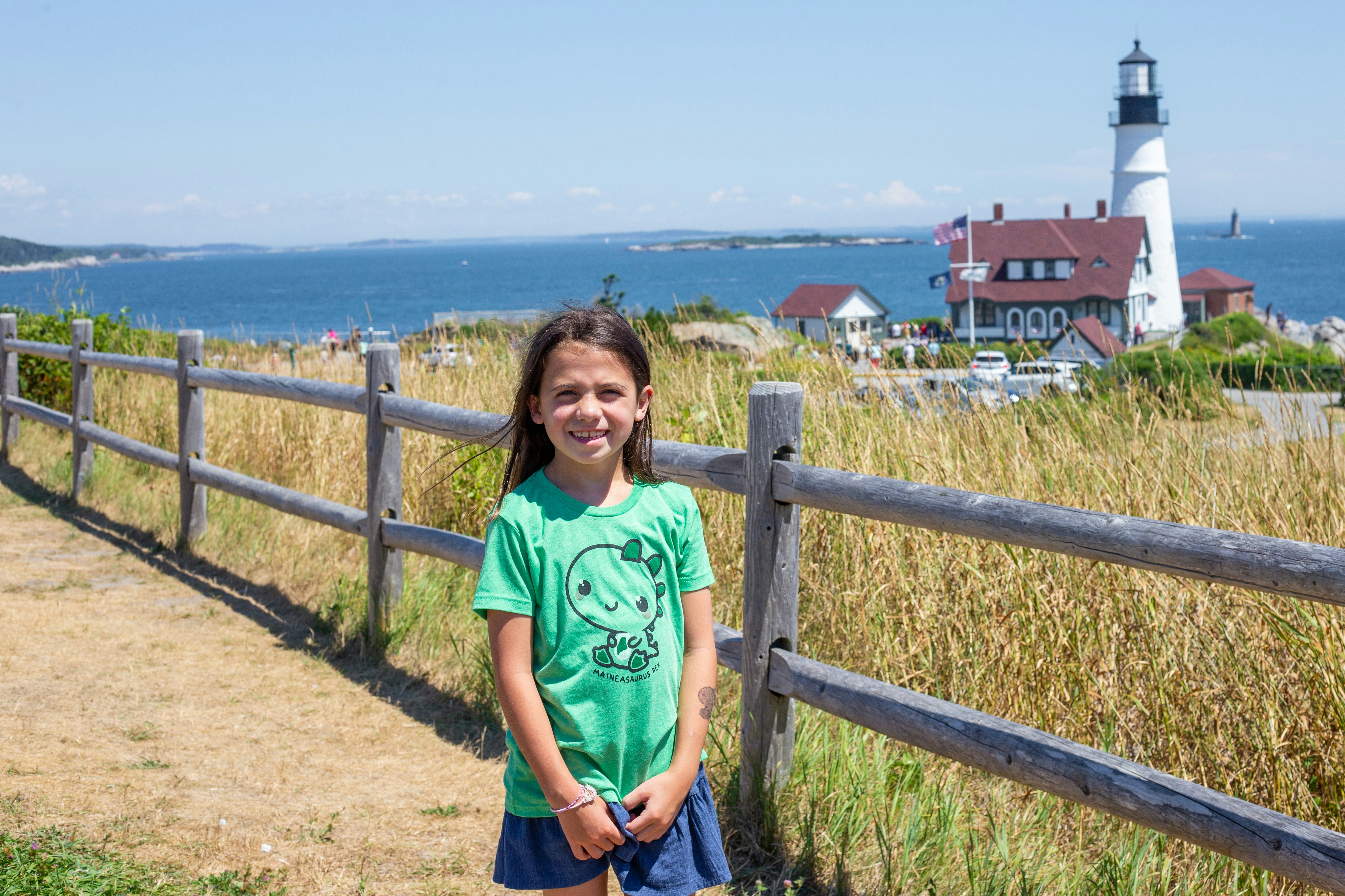 Green Shirt, Lighthouse Horizon: A Seaside Portrait Along a Weathered Fence