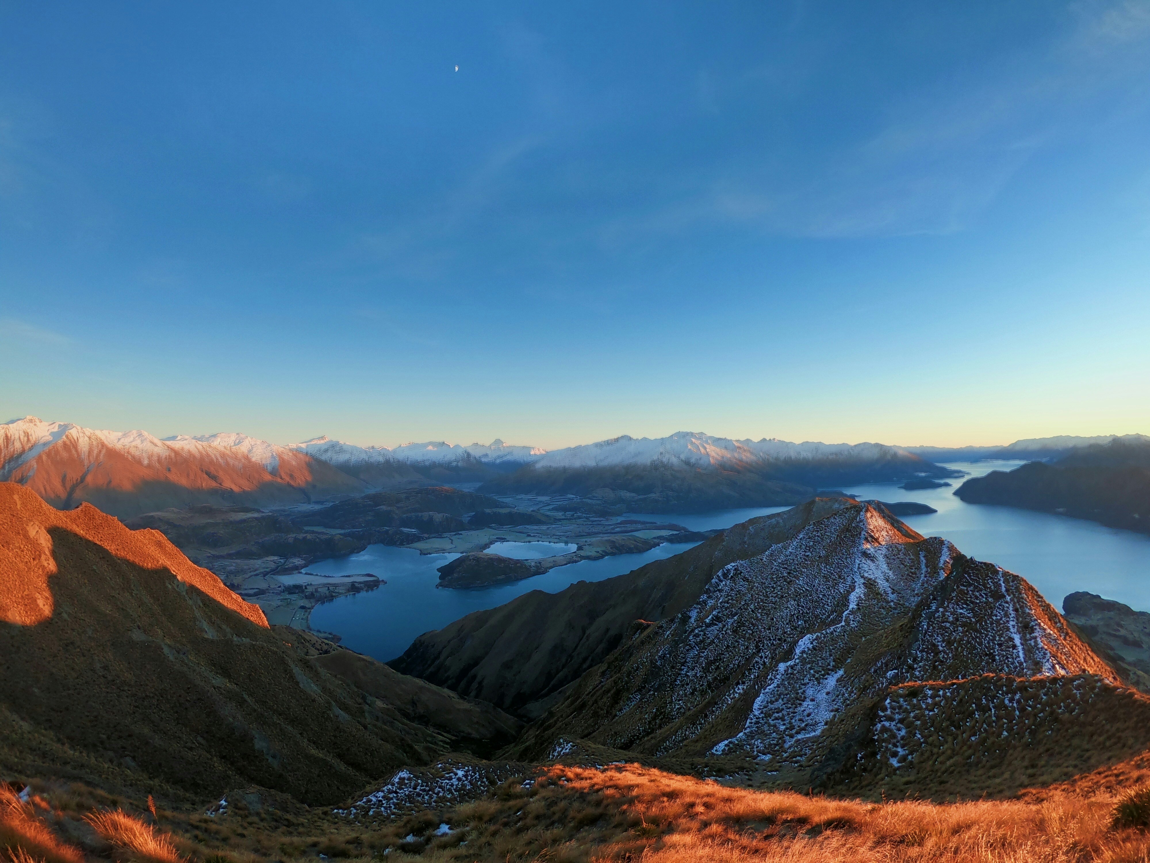 Sunrise illuminating snow-dusted peaks and serene lake at Roy's Peak, New Zealand.