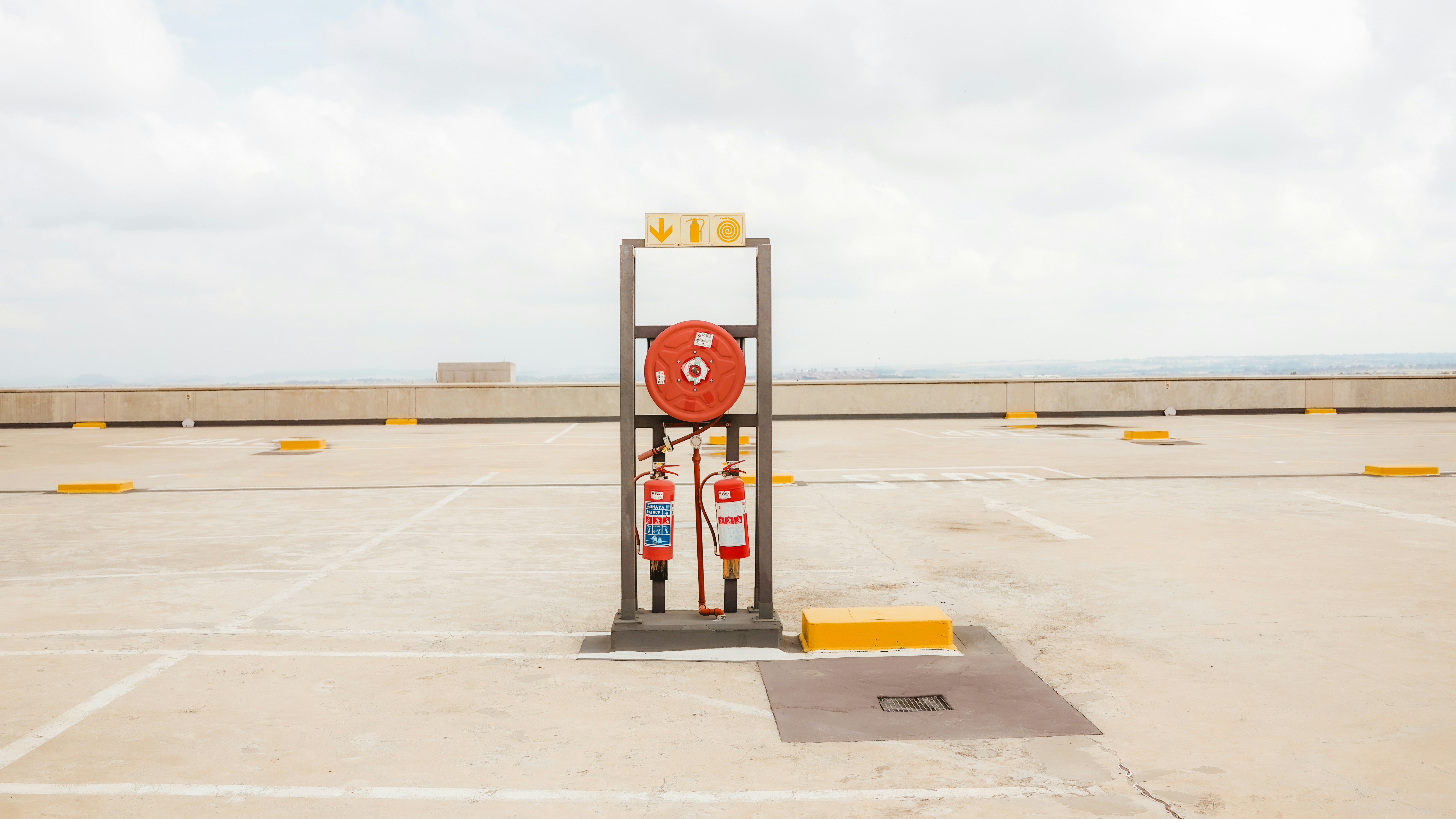 Lonely fire hydrant station on a vast, empty rooftop parking lot under a cloudy sky.