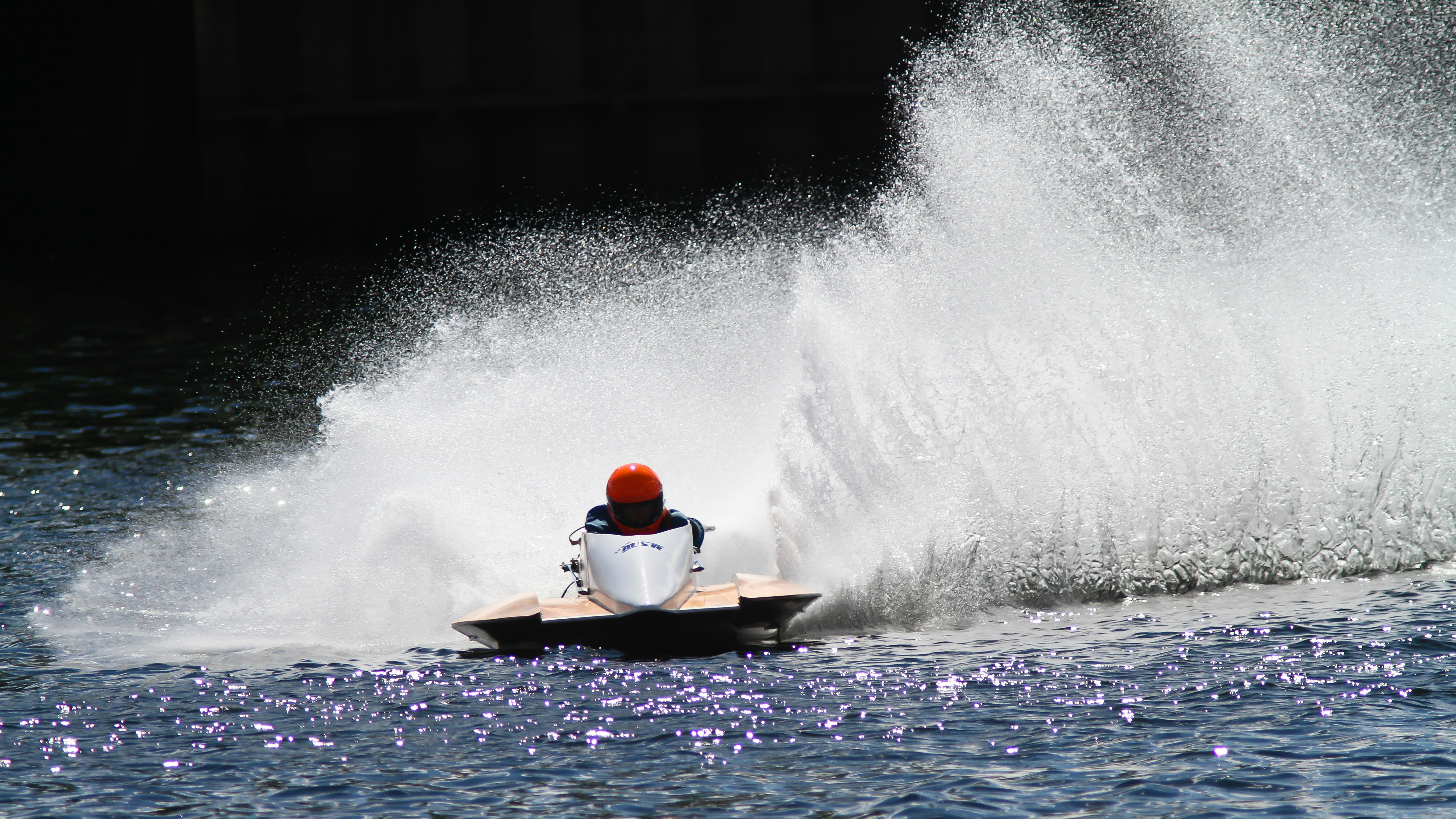 Person on a jet ski creating a large splash, with sunlight glistening on the water.