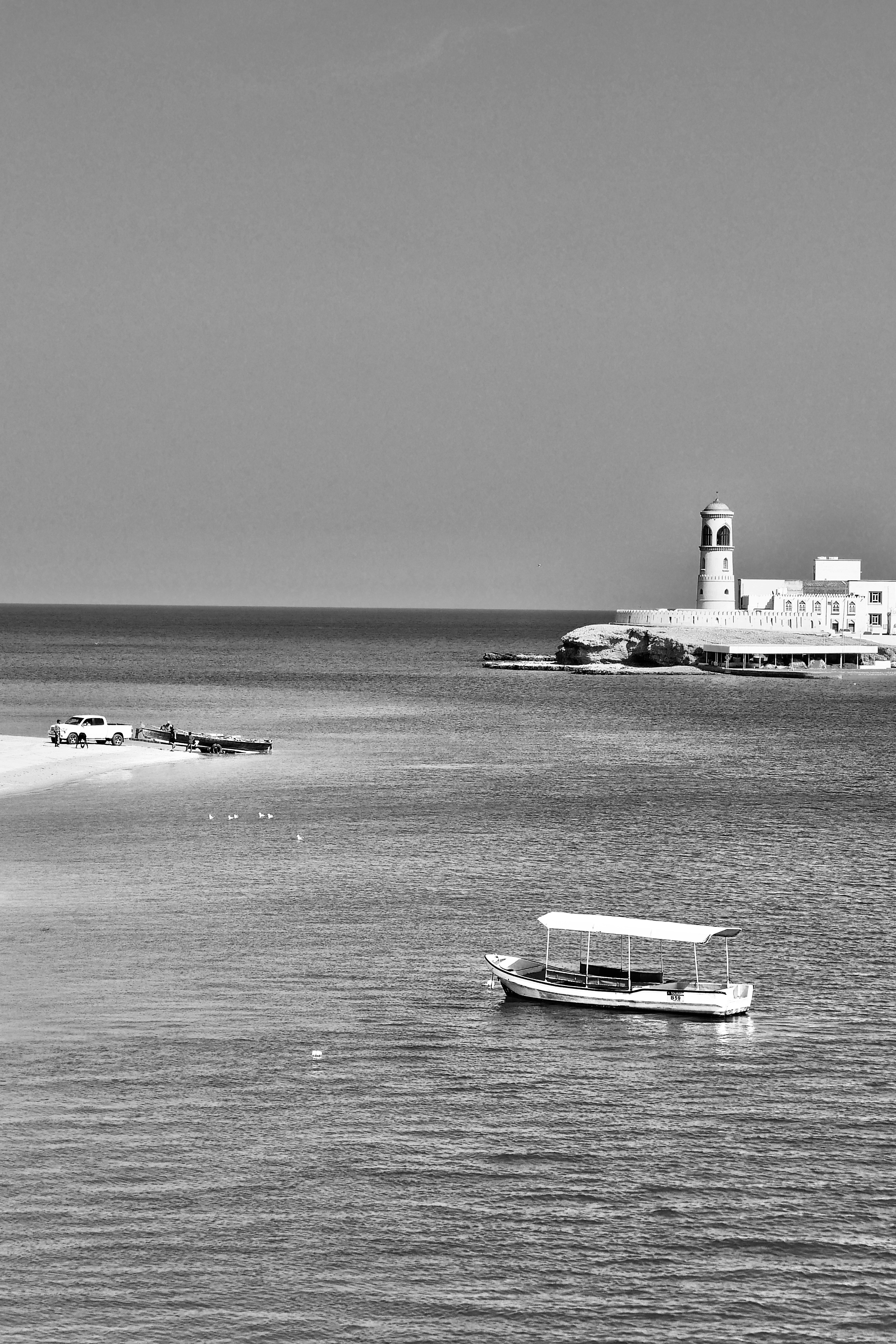 A tranquil harbor scene featuring a lighthouse and a small boat, set against a calm sea. The image captures the essence of coastal life in monochrome.