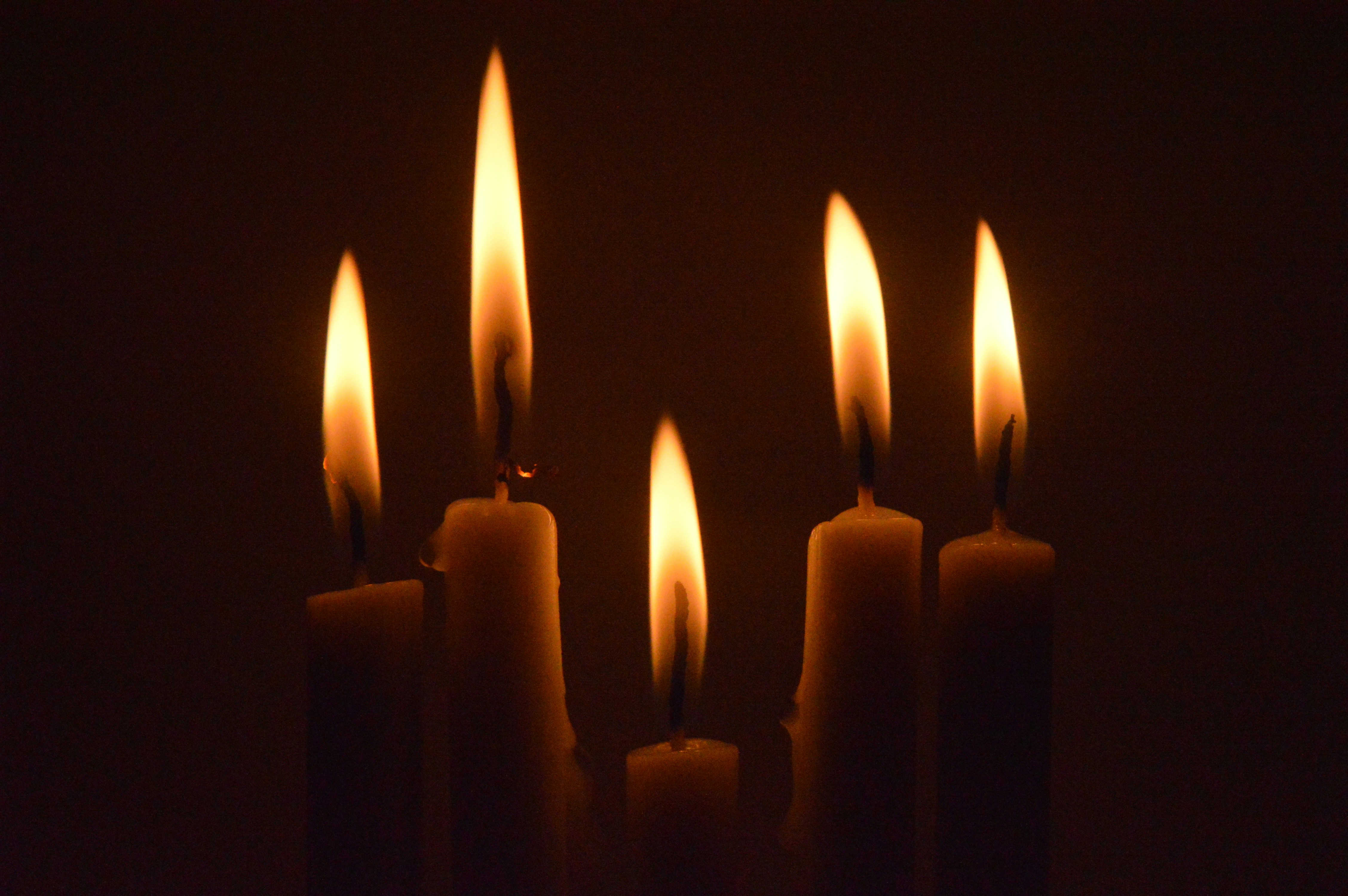 Five lit candles casting warm, flickering light against a dark background, creating an ambiance of tranquility.