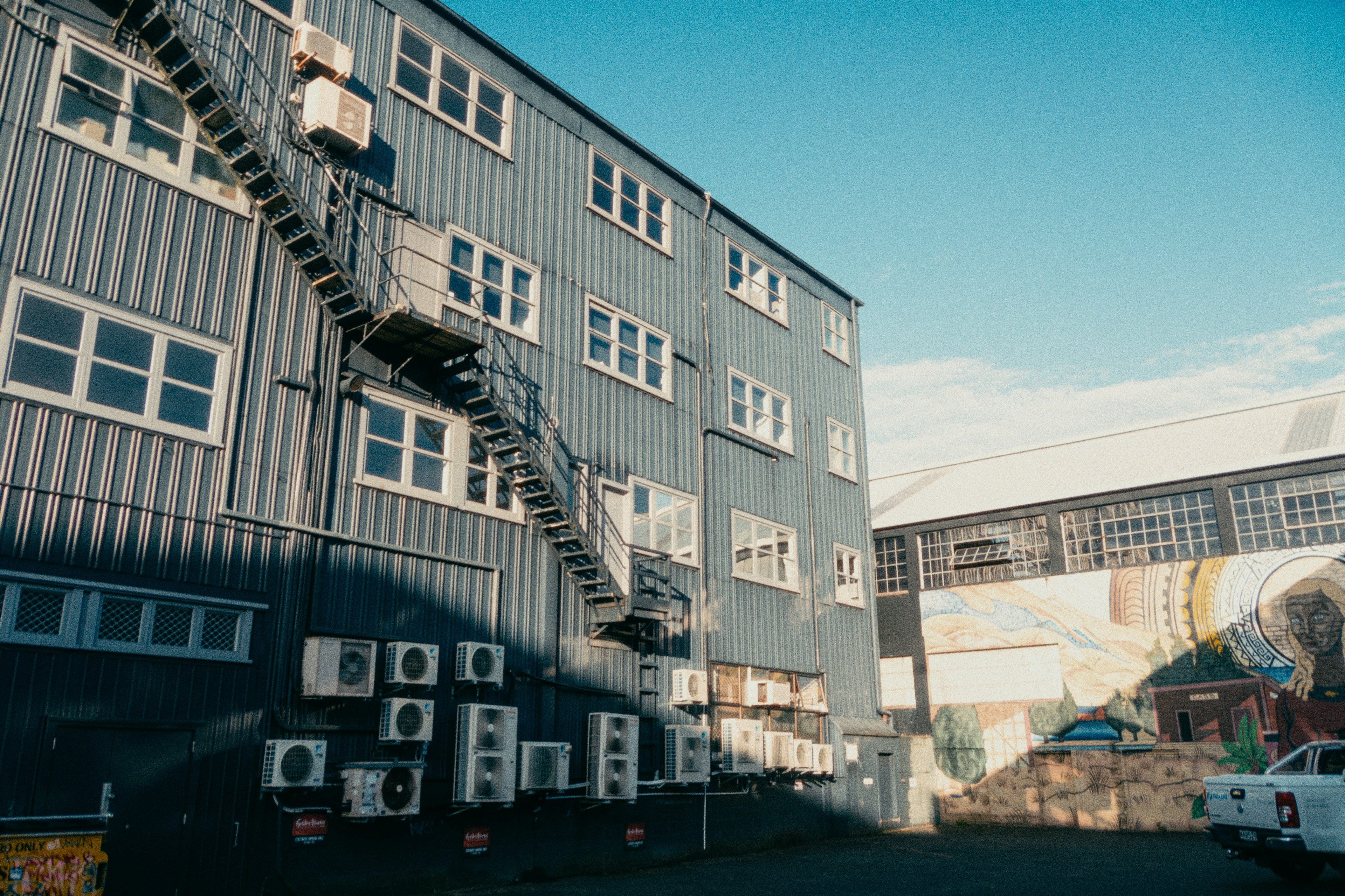 Sunlit Corrugation: Fire Escape Looming Over an Air-Conditioned Facade