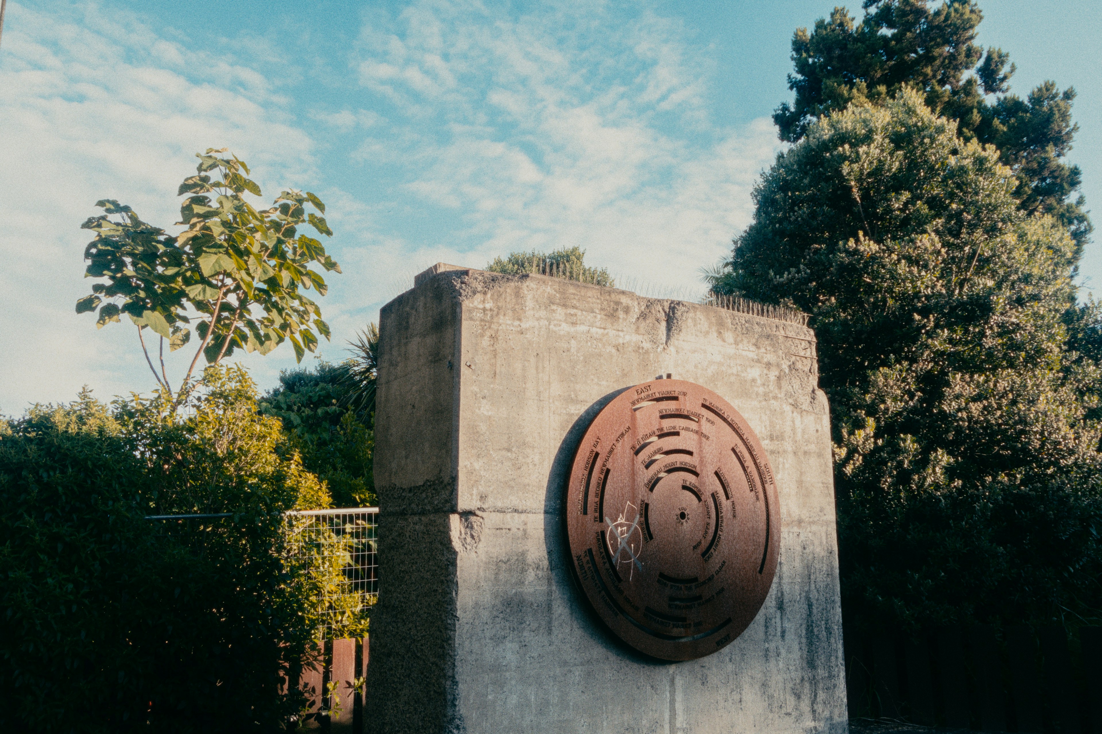 Rust-Red Circular Vent Anchoring a Concrete Pedestal in a Sunlit Park