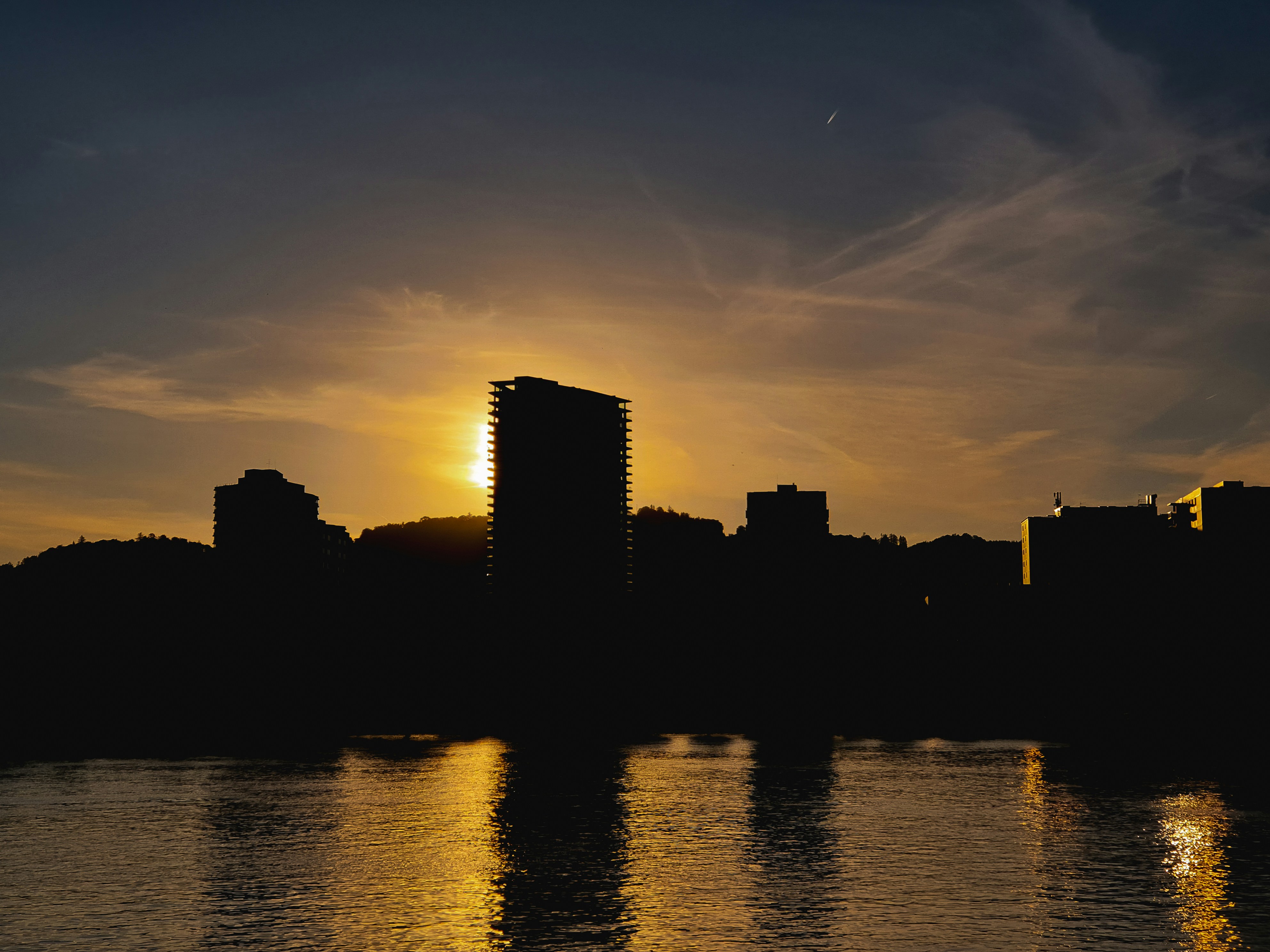 Sunset casting a golden glow behind city skyscrapers reflecting on a tranquil river.