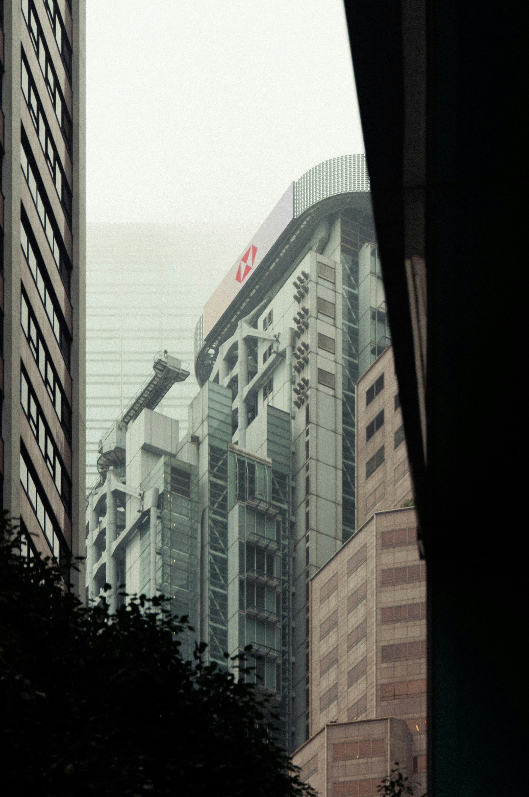 Modern skyscraper framed by adjacent buildings against a foggy skyline.