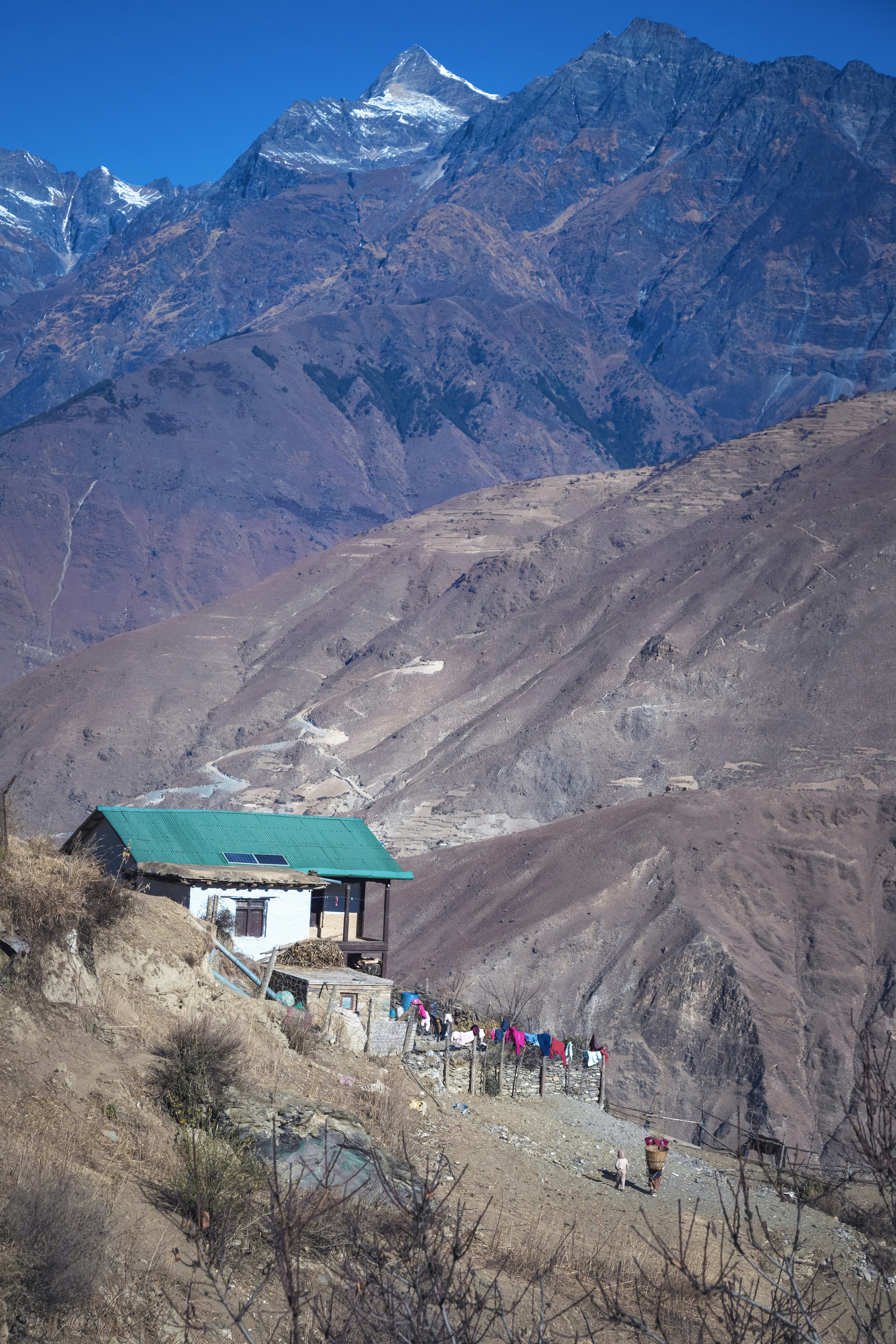 Green-roofed refuge clinging to a sunlit hillside beneath towering alpine peaks