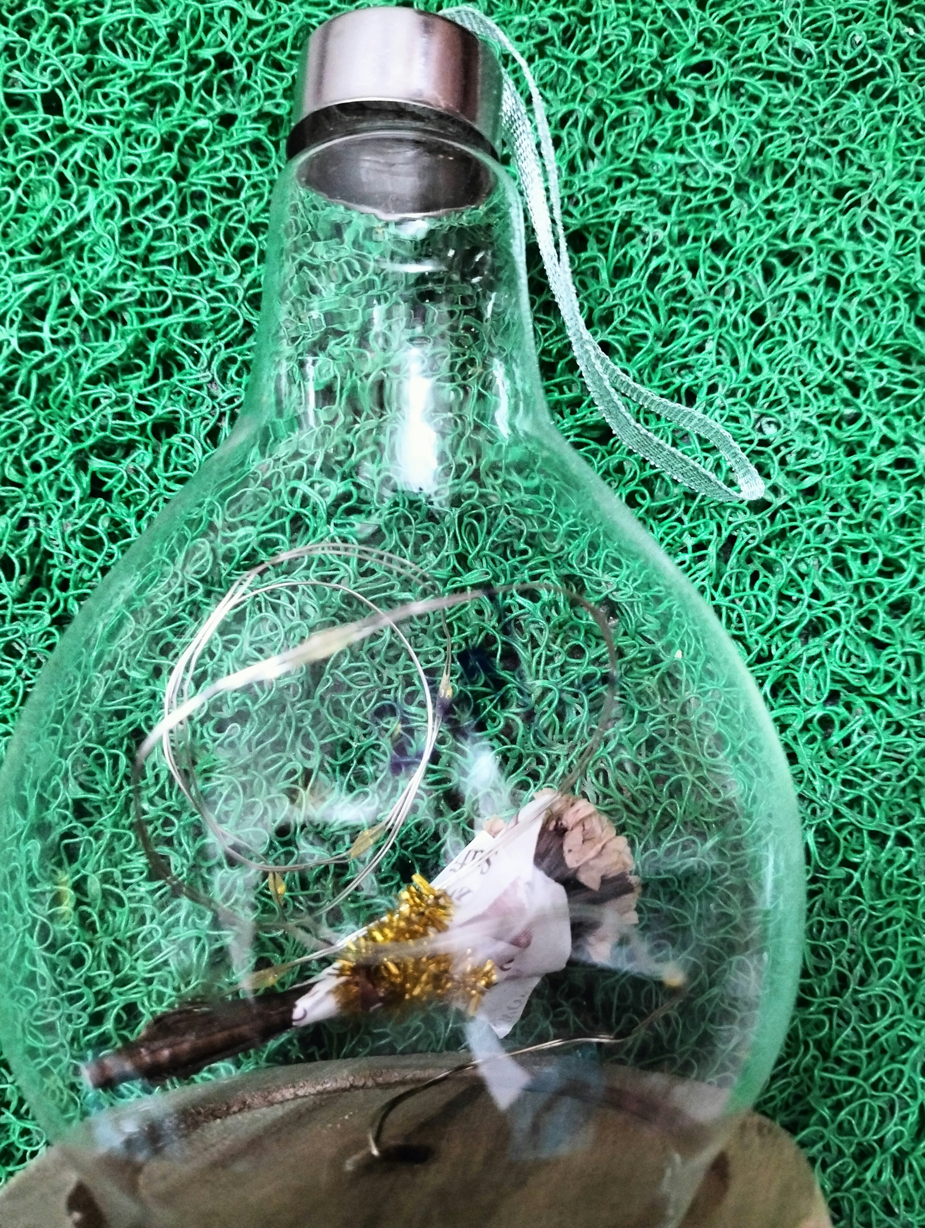 A Teardrop Glass Bottle with Tiny Trinkets Captured on Green Mat