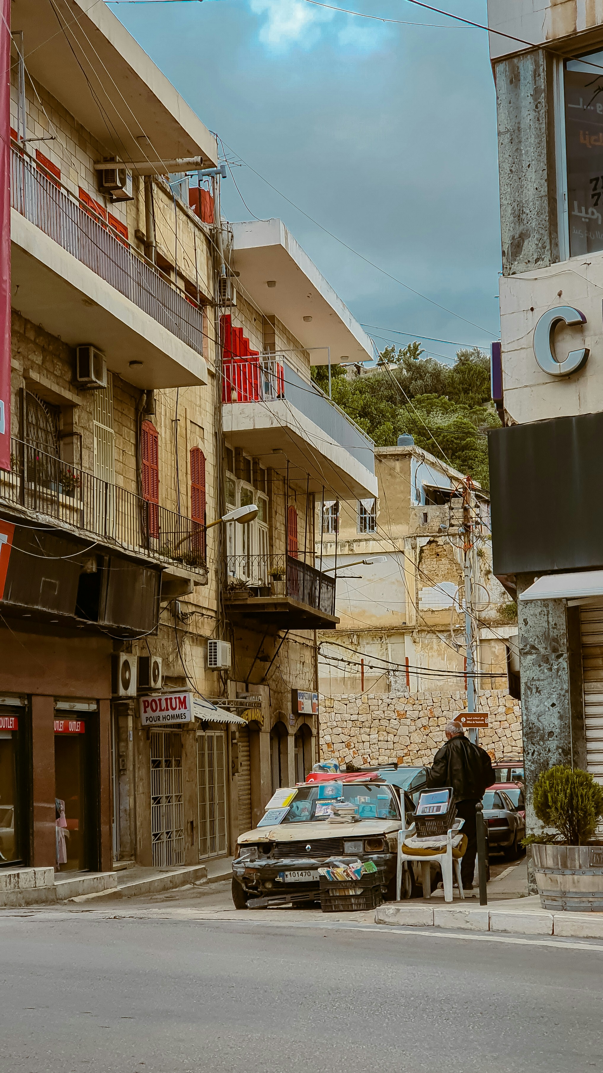 Busy urban street with a weathered building facade, parked taxi, and a man near a chair by the sidewalk; a sense of daily life in a small town market area.