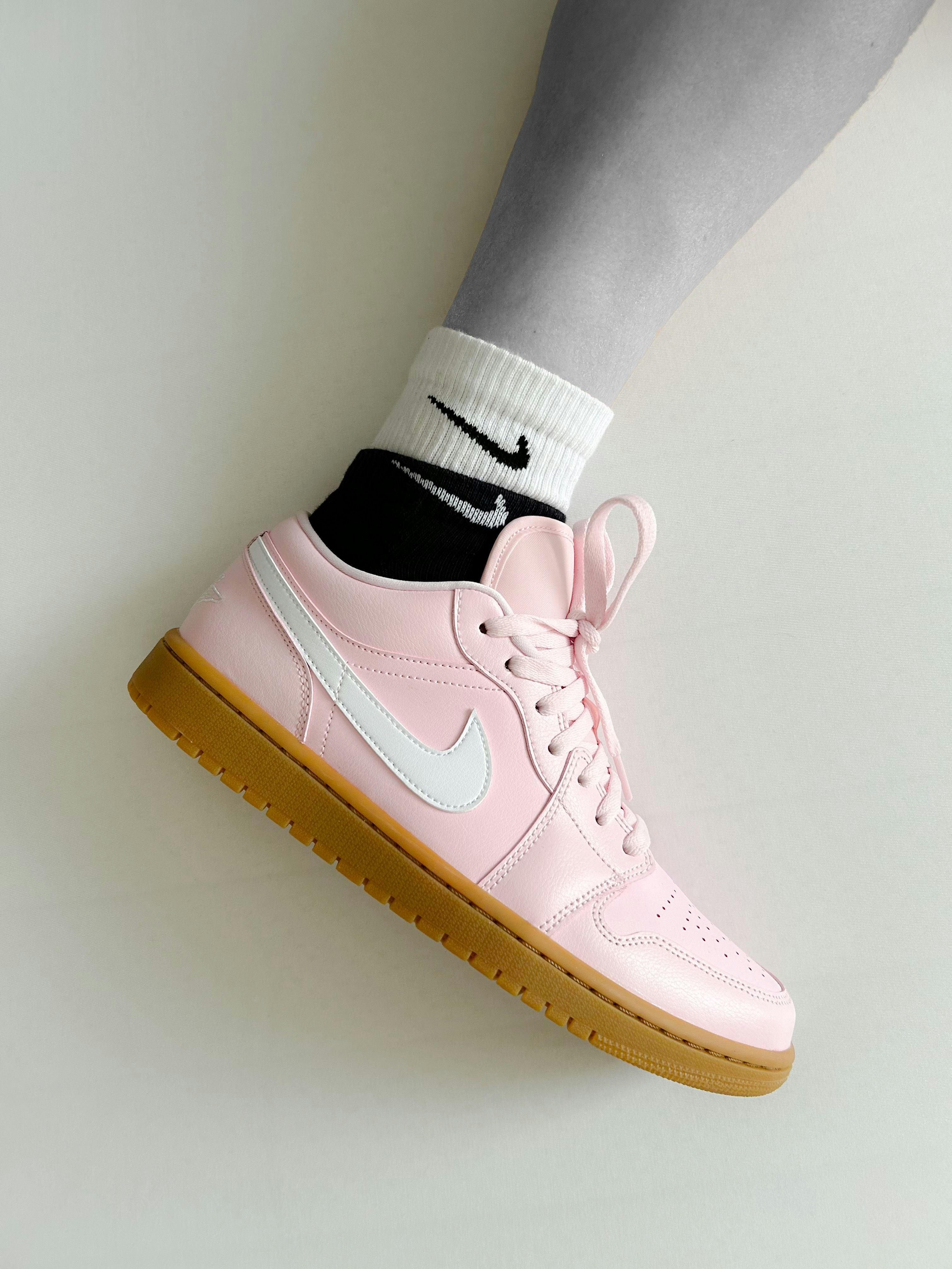 Pink Nike Dunk sneaker with white swoosh and gum sole, paired with a black Nike sock, suspended over a pale background.