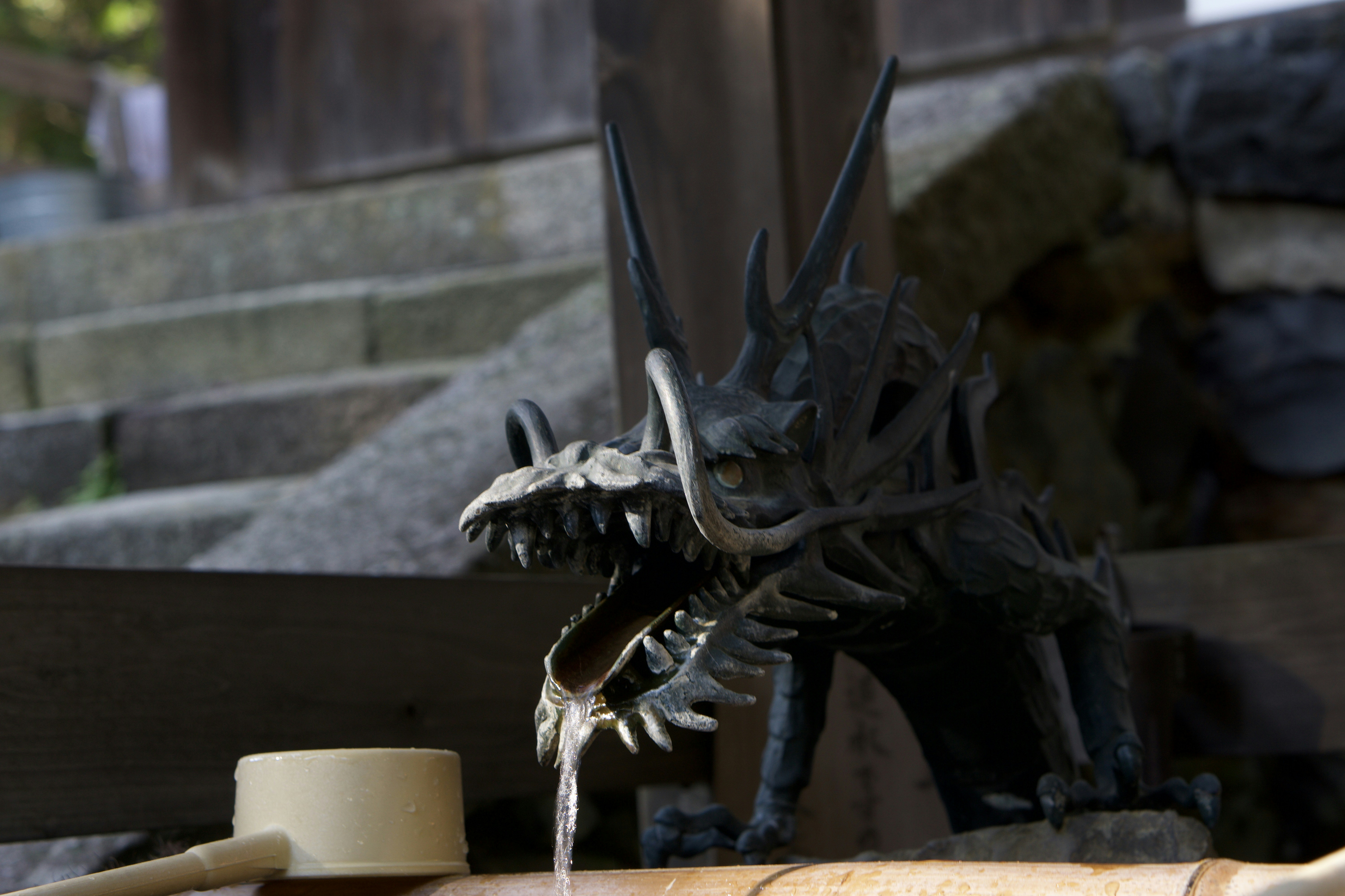 Bronze dragon sculpture spouting water in a serene garden setting, surrounded by stone steps and natural elements.