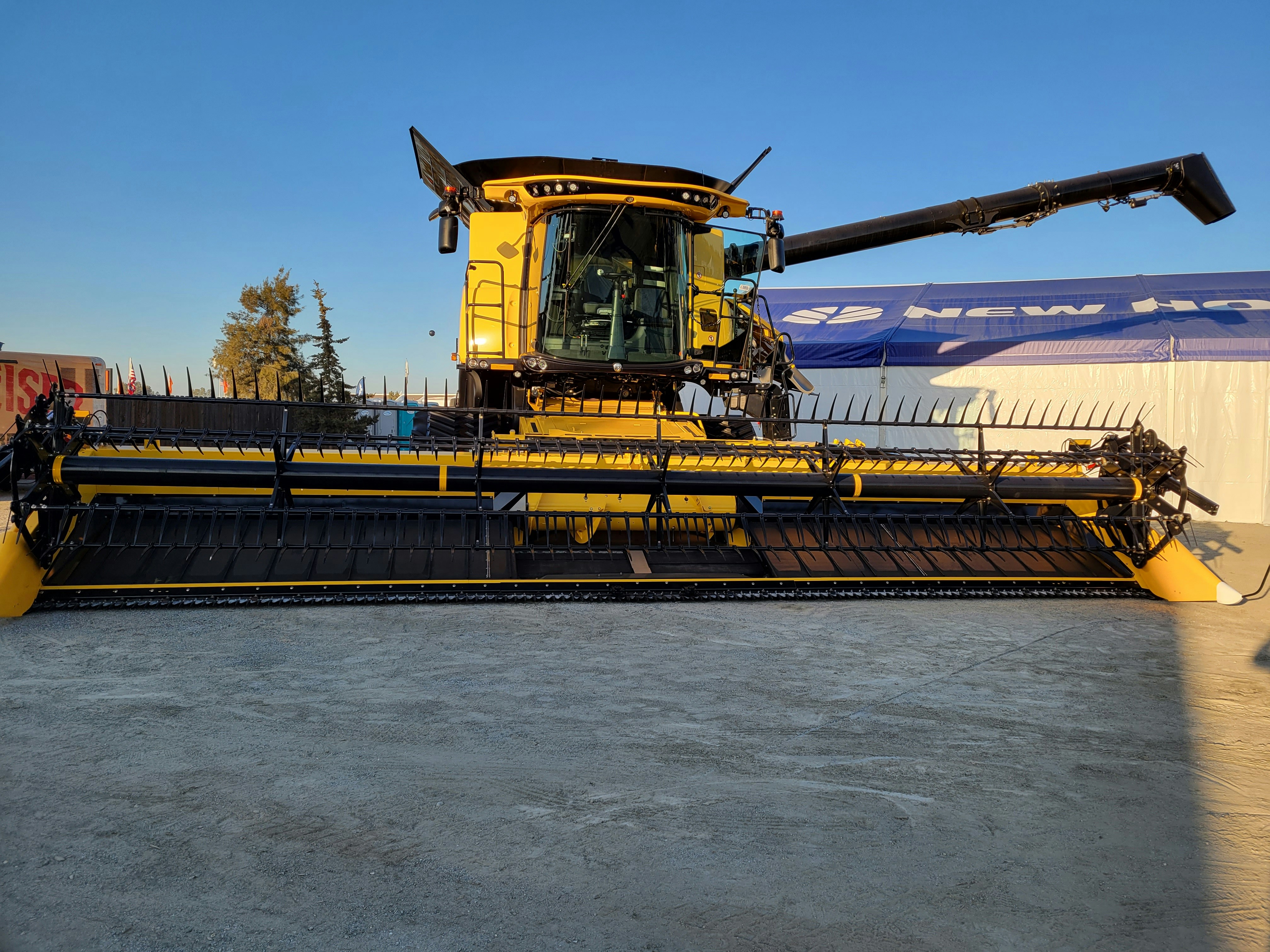 Large yellow combine harvester parked on concrete under a clear blue sky.