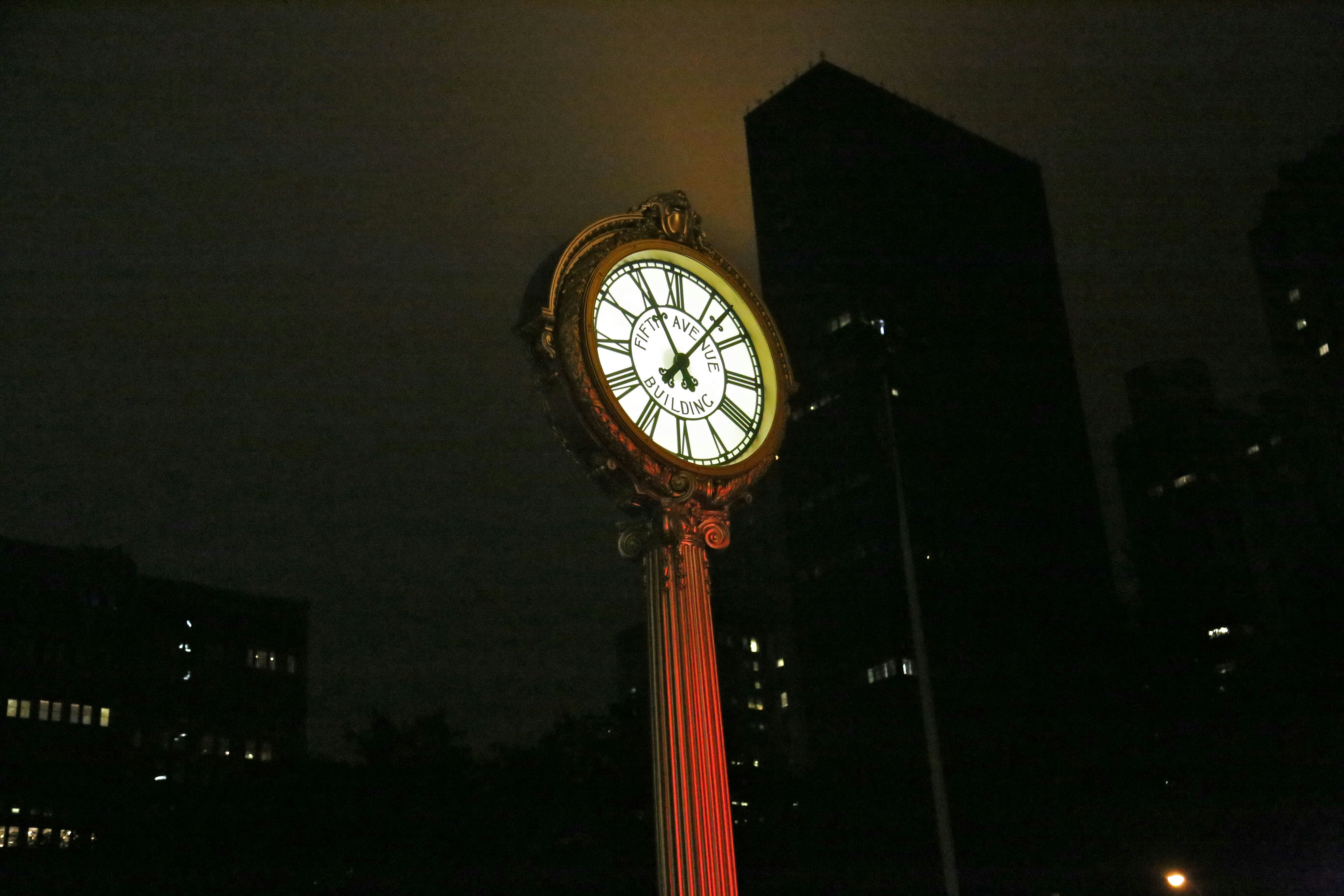 Midnight Clock on a Crimson Post Amid Quiet Skyscrapers